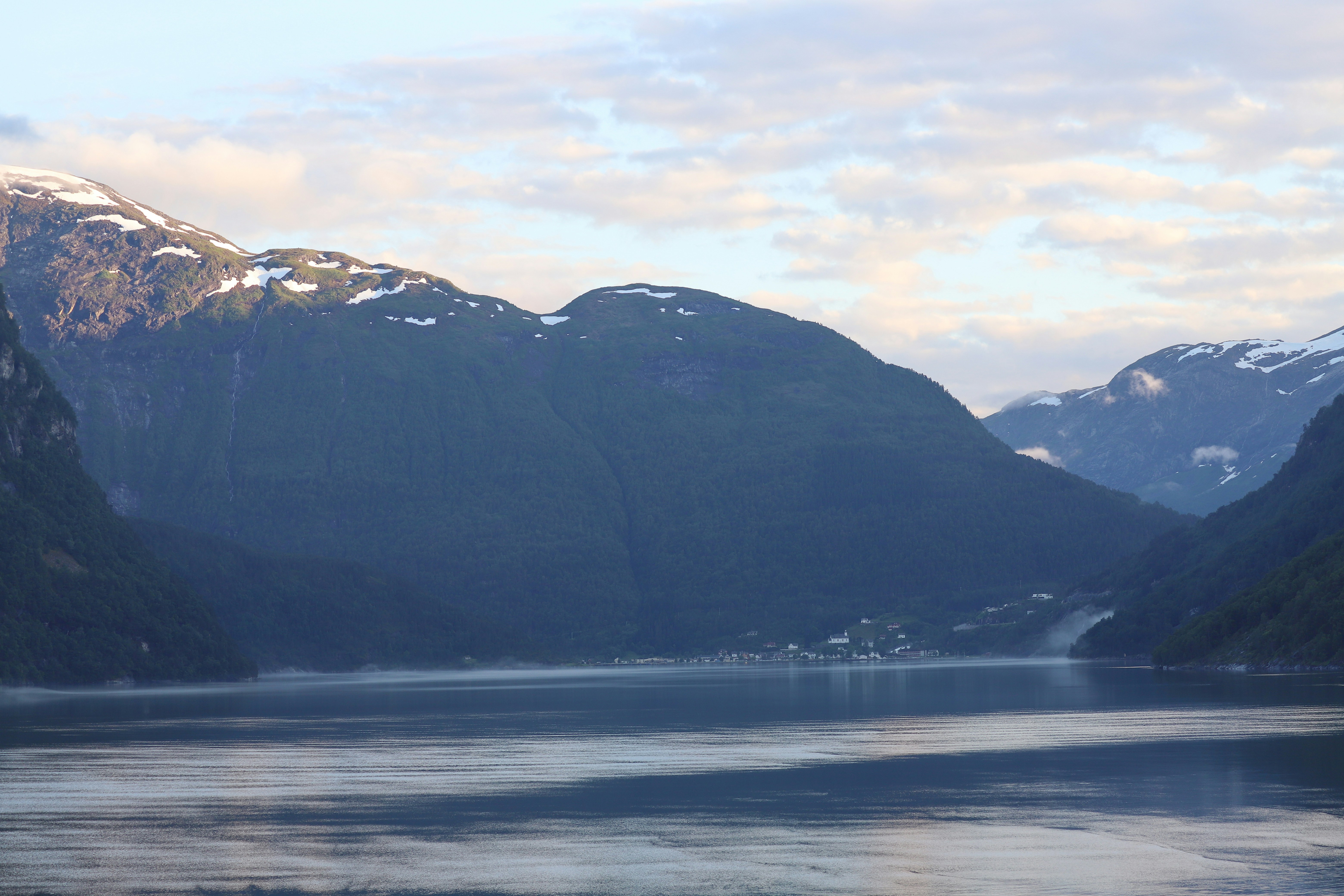 Majestic fjord landscape with snow-capped mountains reflecting in calm waters under a soft sky.
