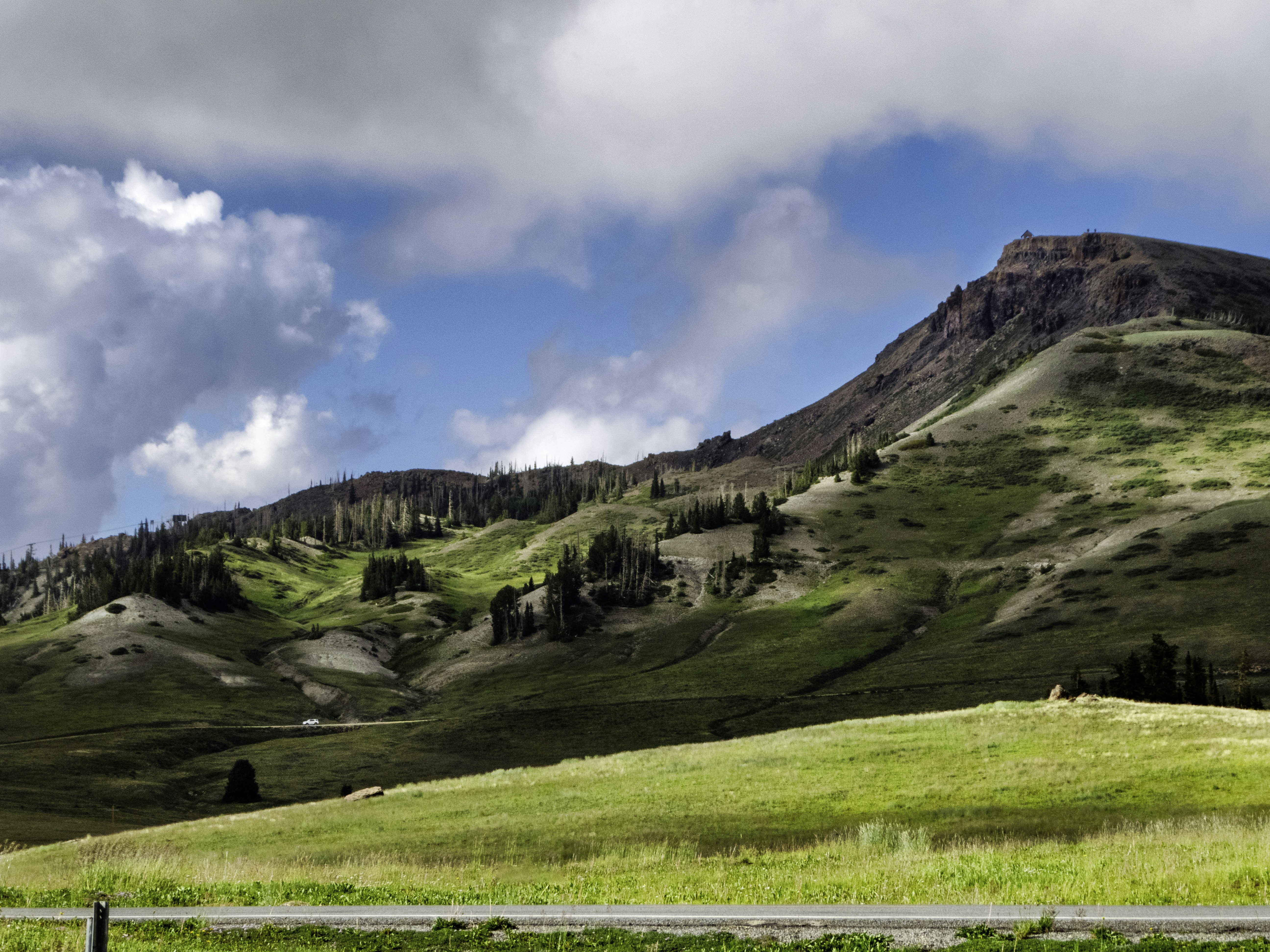 Lush green hills rolling beneath a majestic mountain under a partly cloudy sky. The scene captures the serene beauty of nature's landscape.