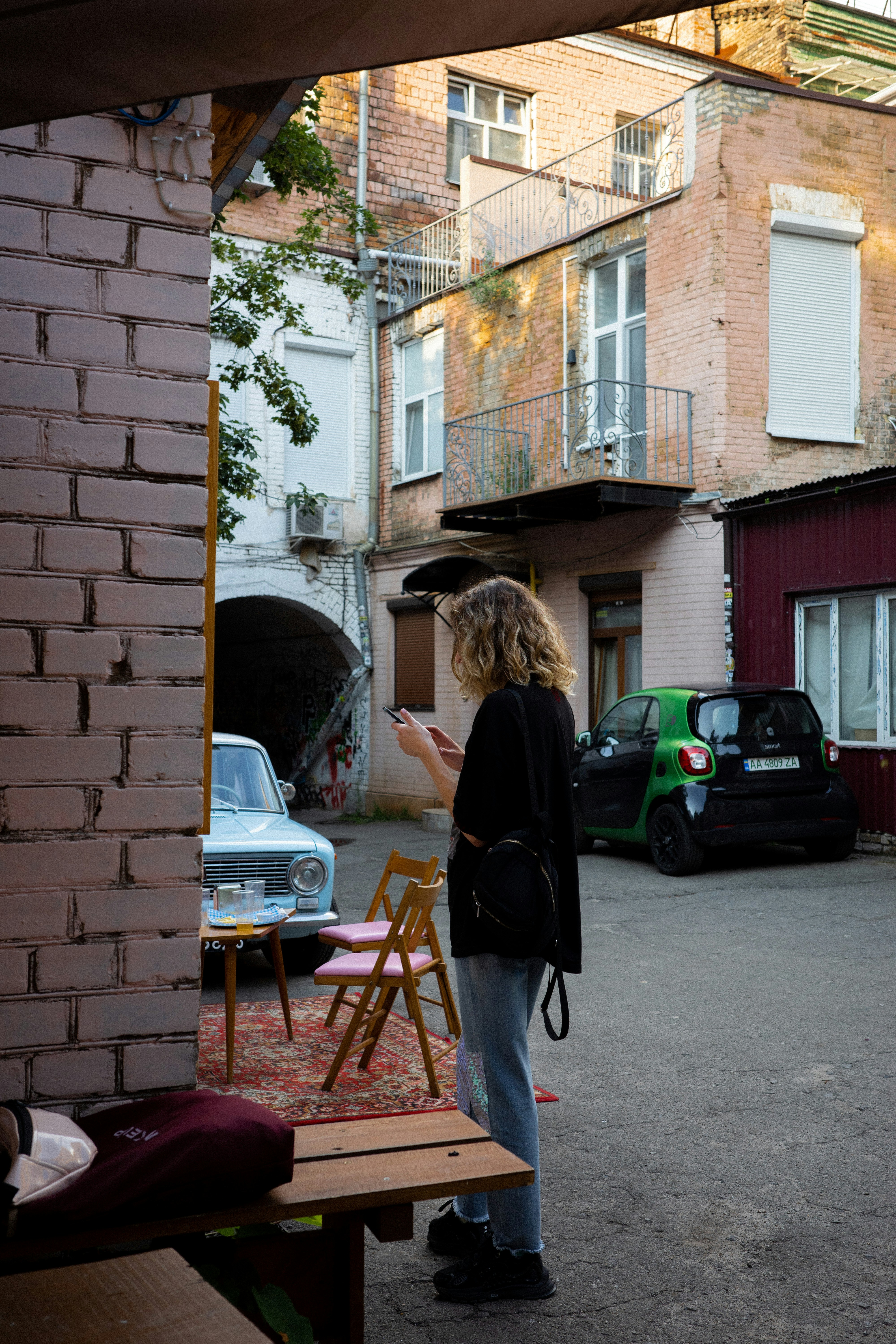 Urban doorway encounter: a woman faces away with a handset amid sunlit bricks