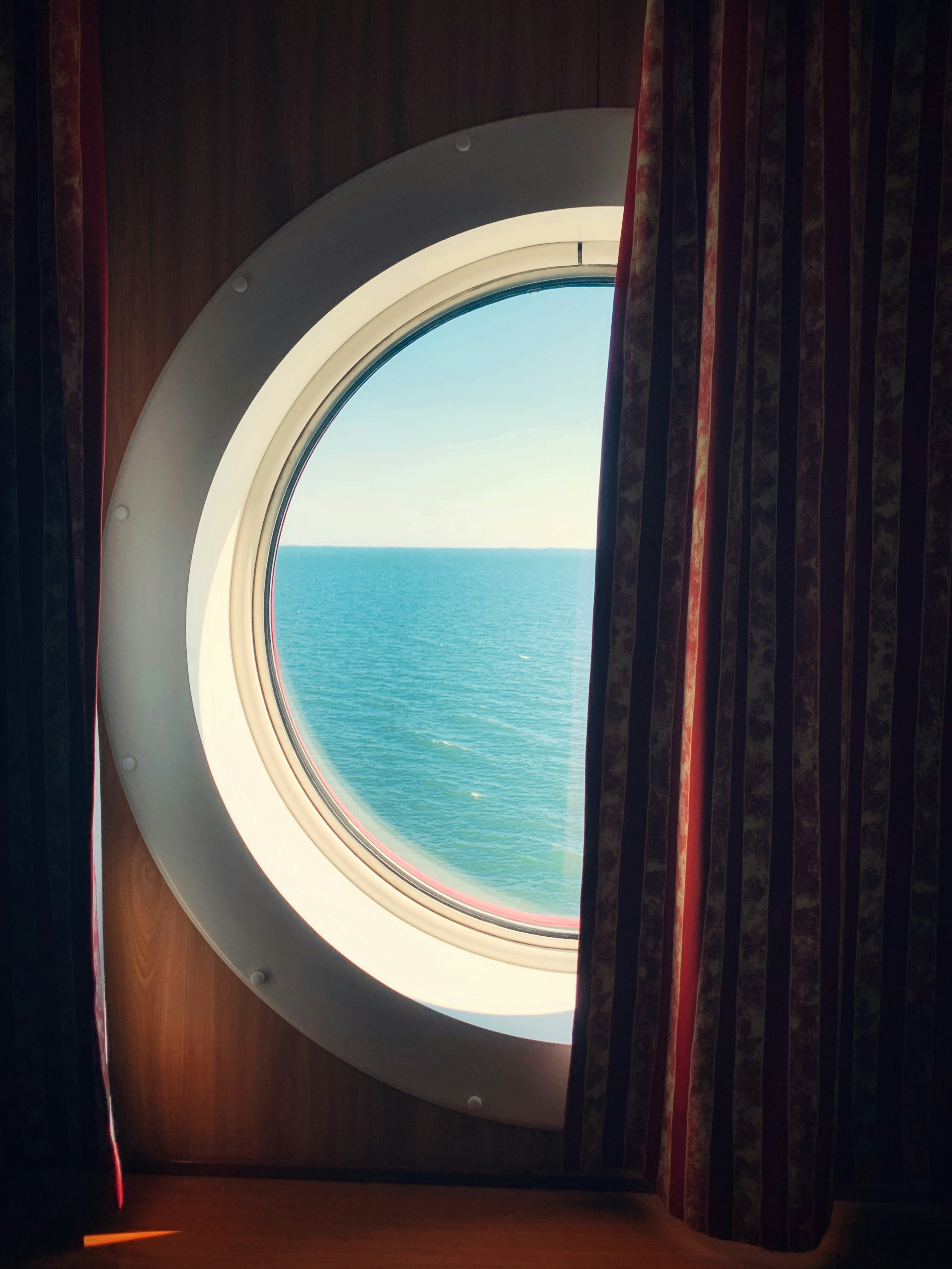 Porthole Vista: Ocean Horizon Peeking Through Velvet Curtains