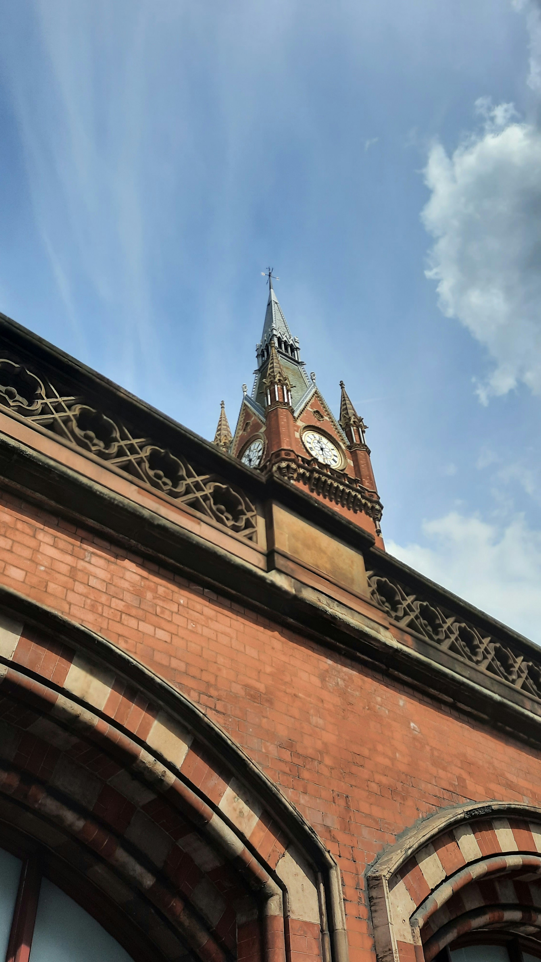 Historic clock tower rising above a brick archway under a blue sky with wispy clouds.