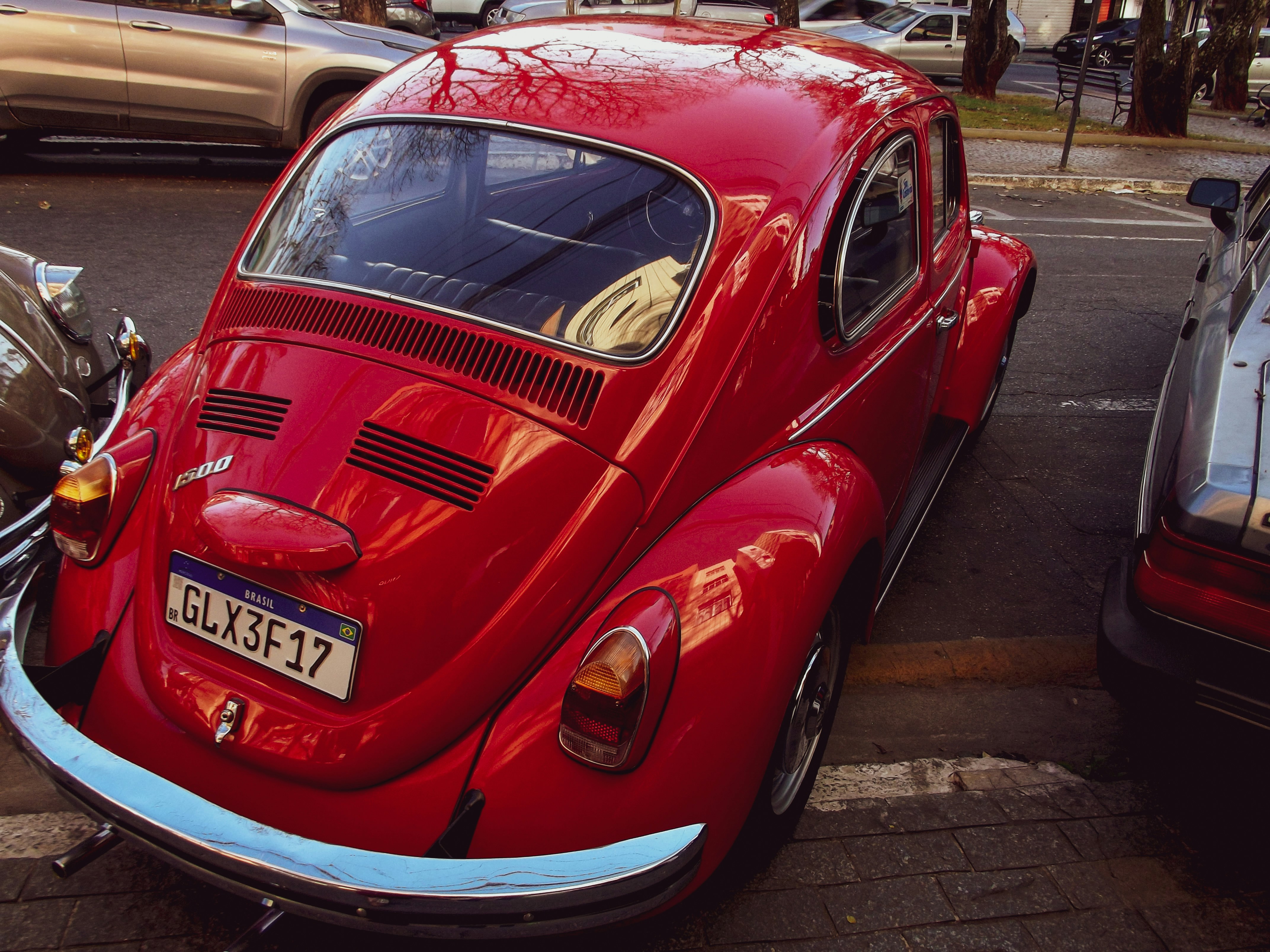 Classic red Volkswagen Beetle parked beside modern cars in a city setting.