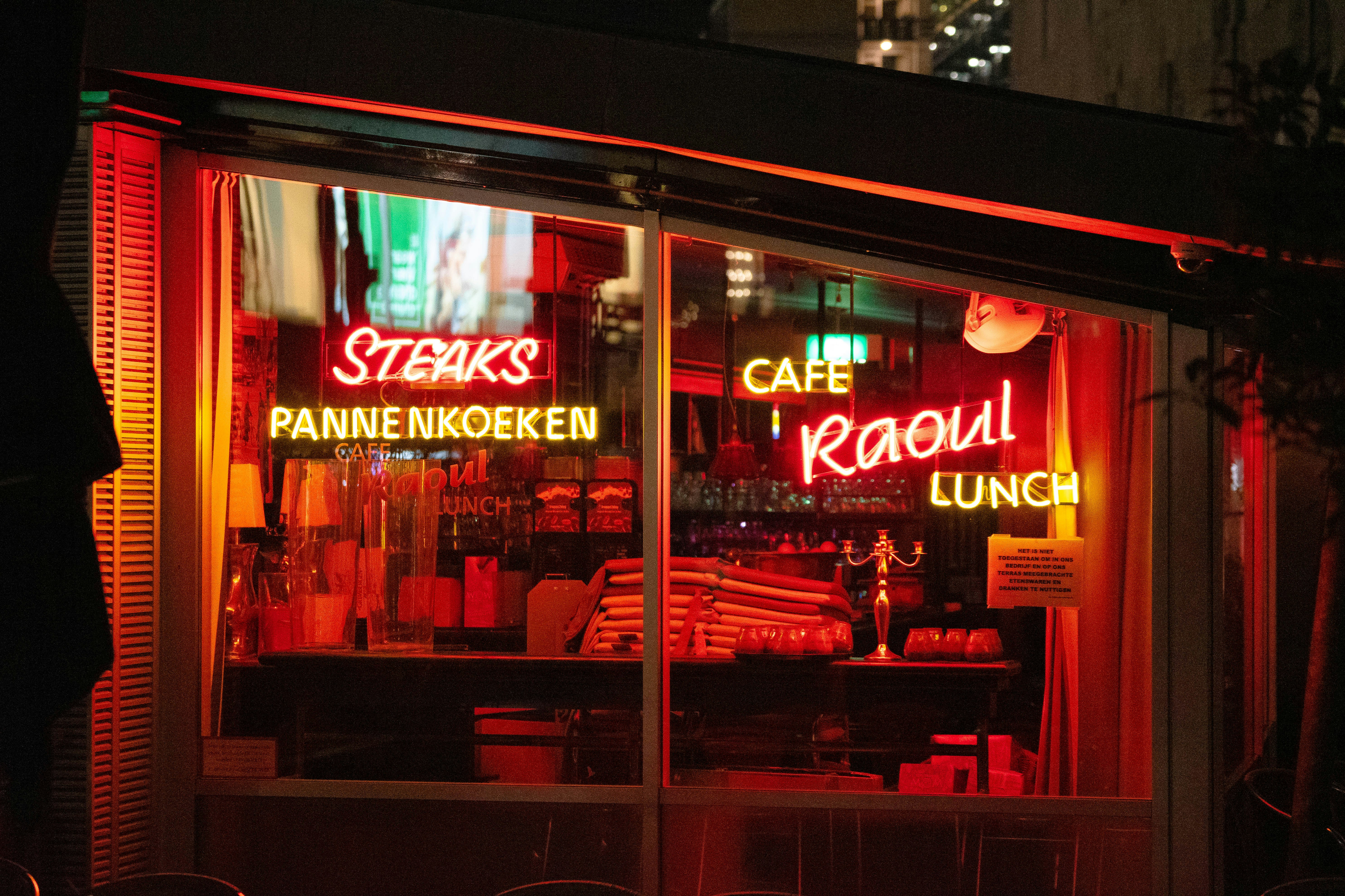 Vibrant neon signs illuminate a cozy café window, showcasing the inviting atmosphere and menu offerings. The warm glow enhances the urban night scene.