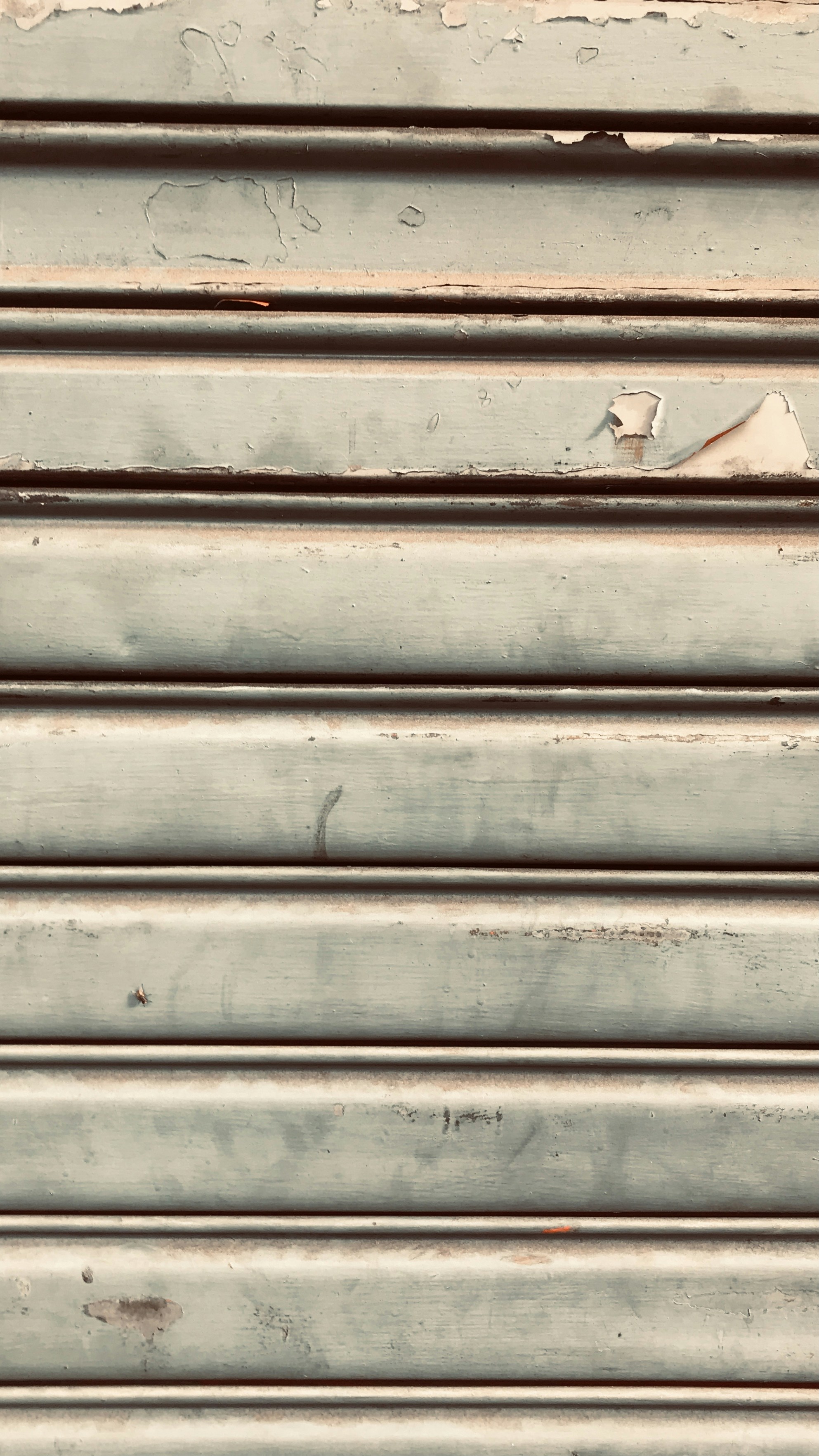 Close-up of a weathered metal surface with horizontal grooves, showcasing peeling paint and subtle texture variations.
