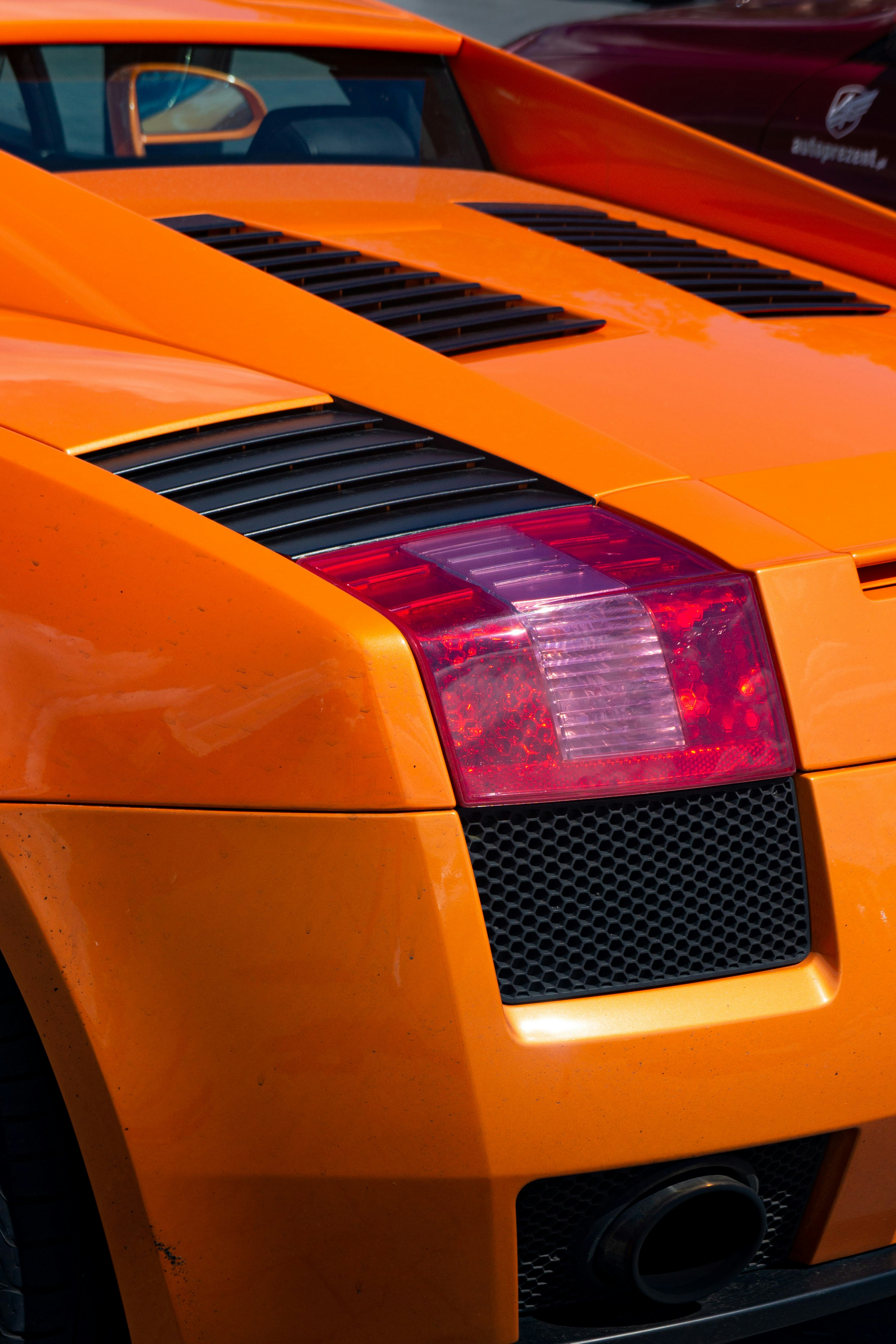 Close-up of an orange sports car showcasing its sleek rear design and intricate detailing. The image highlights the interplay of light and shadow on the vehicle's surface.