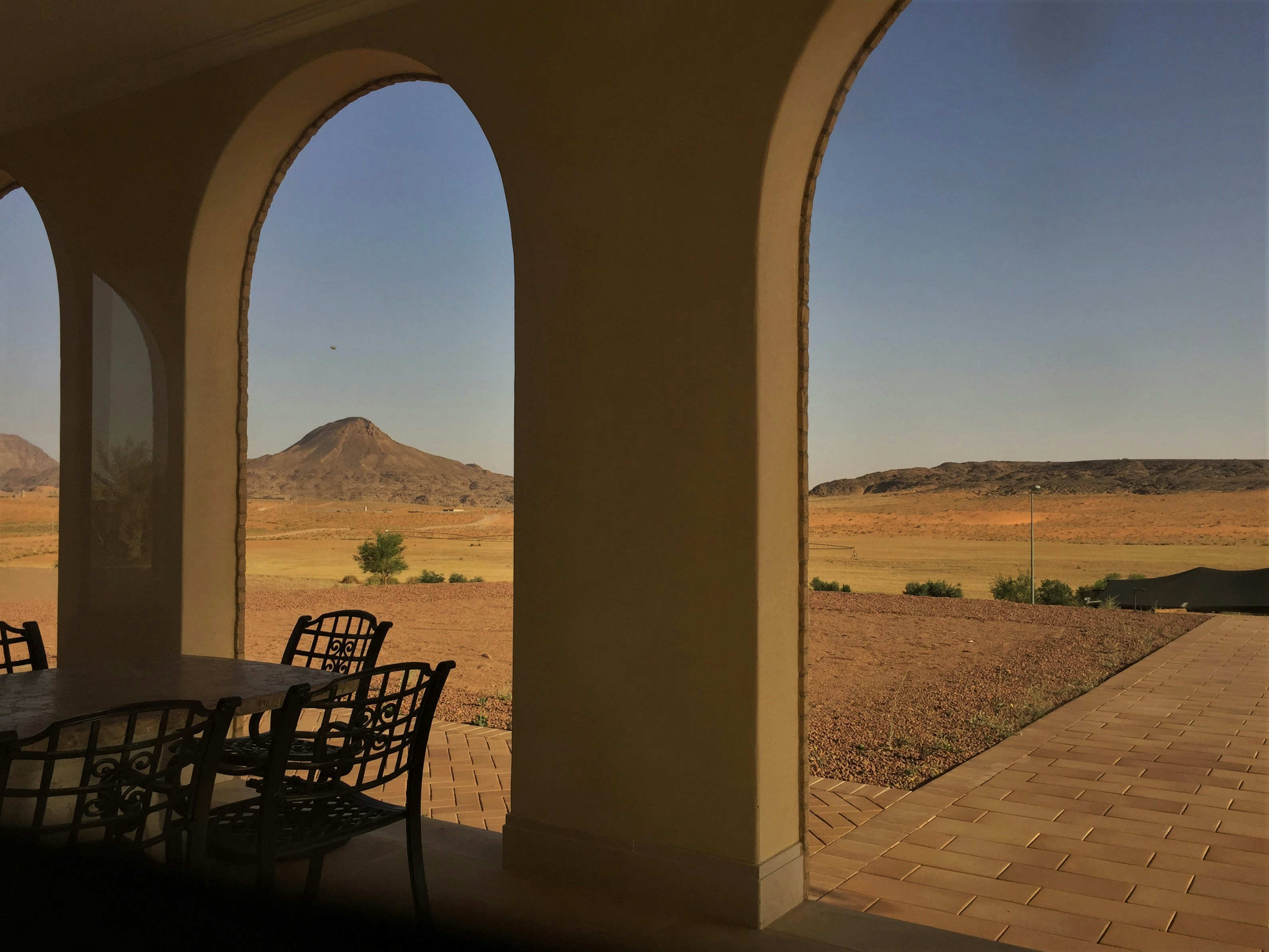 Arched patio frames a distant mountain and desert landscape under a clear blue sky.