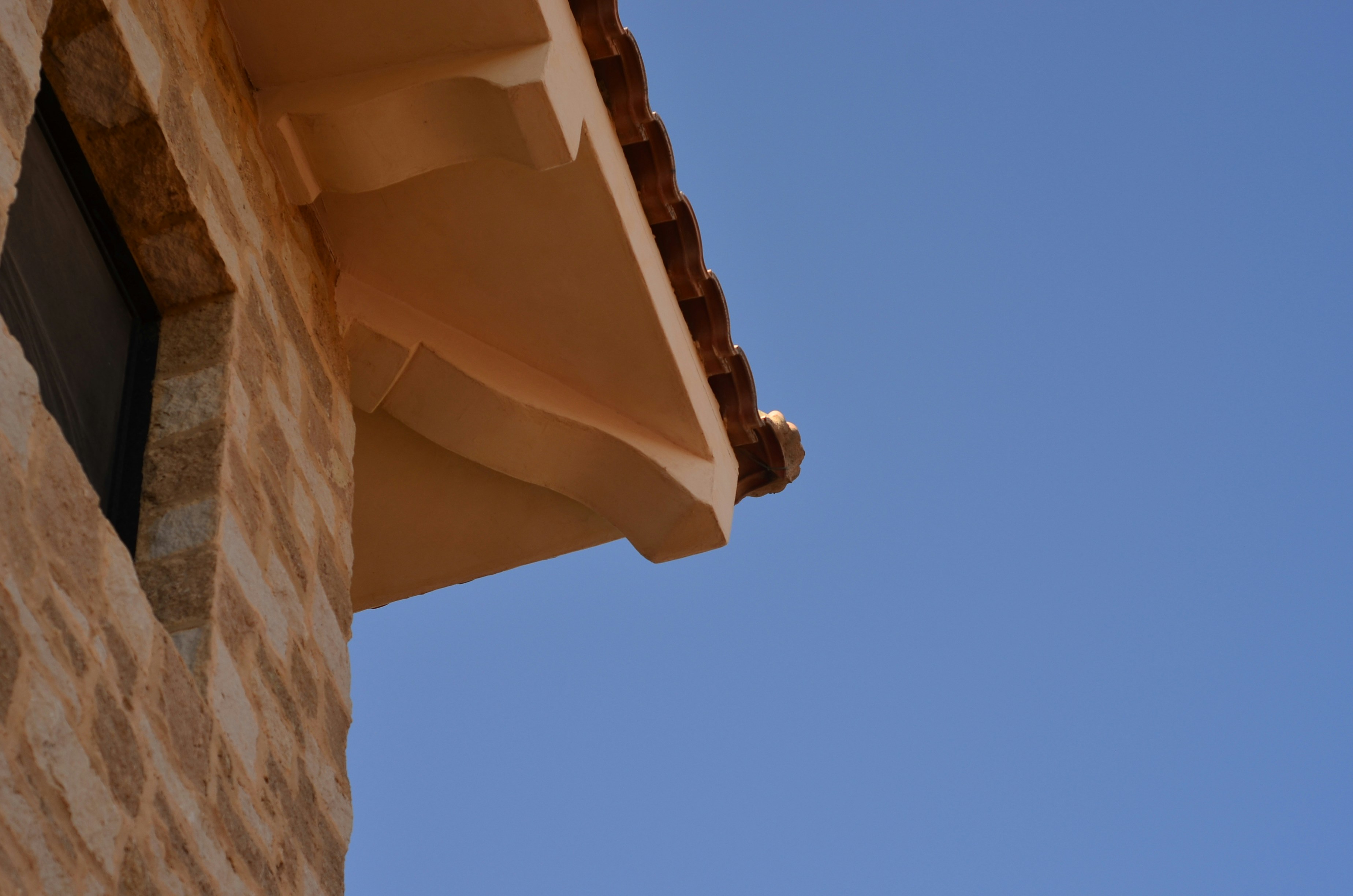 Corner of a stone building roof against a vivid blue sky.
