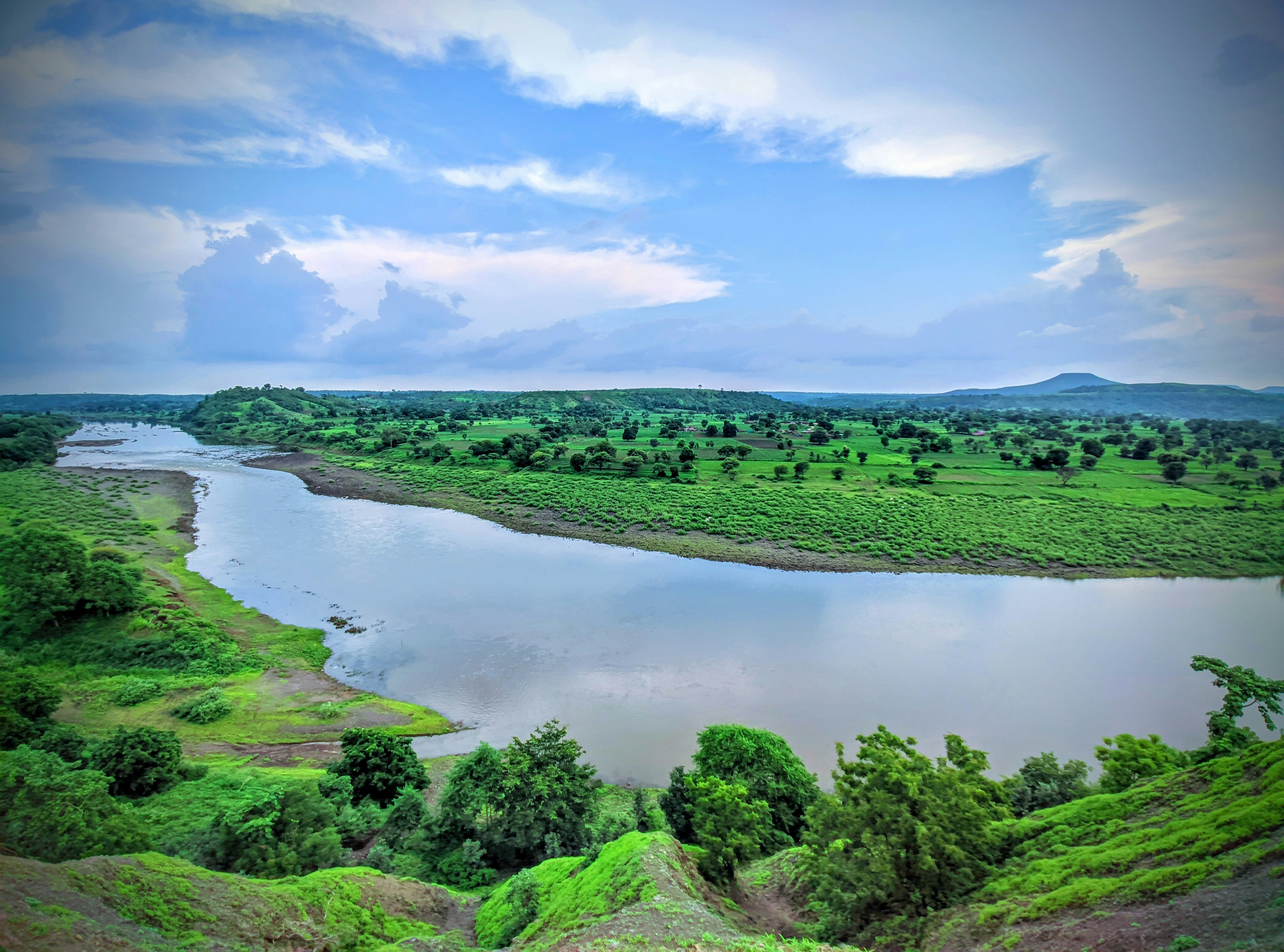 Lush green landscape with a winding river reflecting the sky, framed by distant hills. Ideal for showcasing natural beauty.
