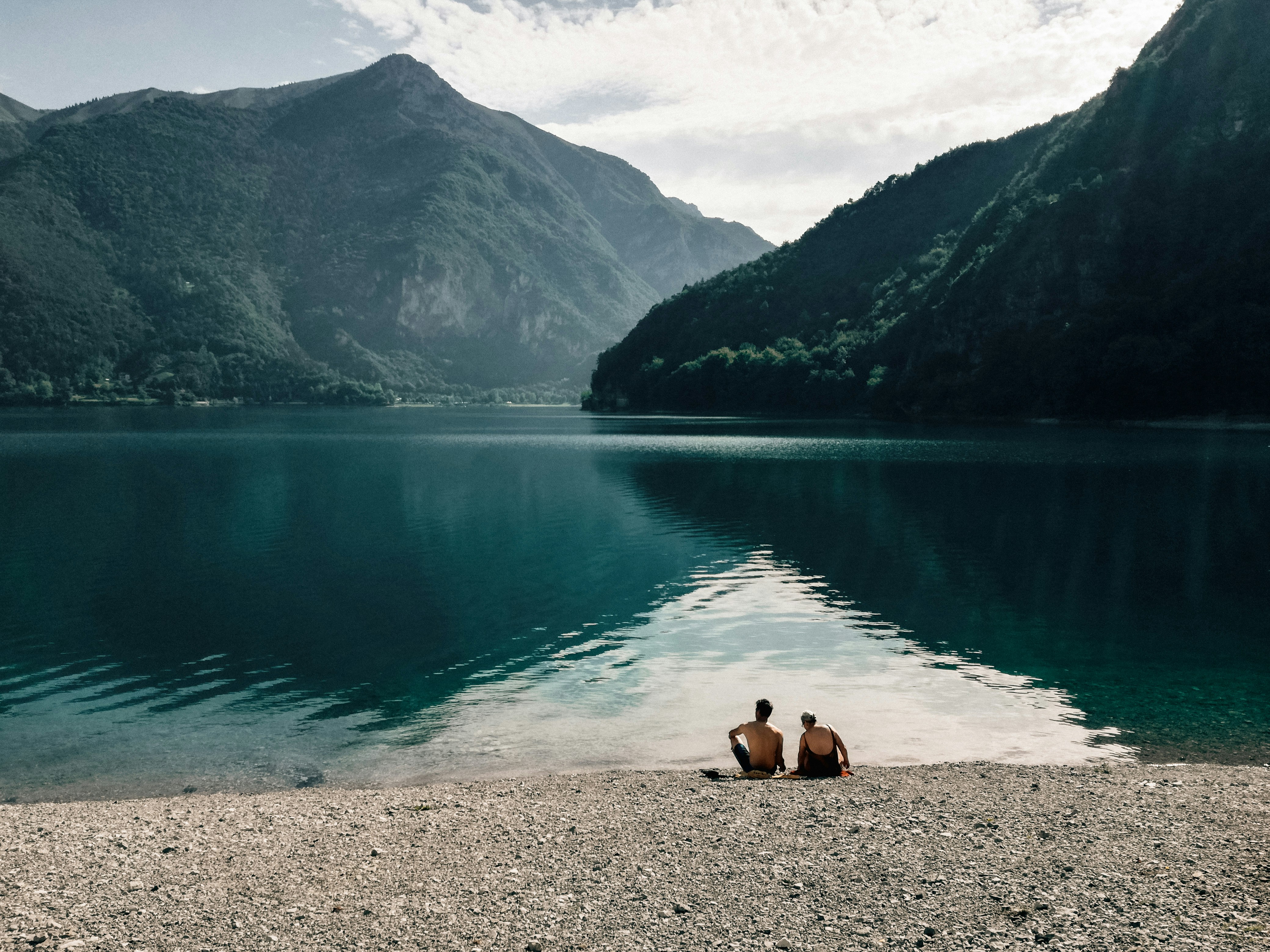Two silhouettes on the pebbled shore as mountains cradle a turquoise lake