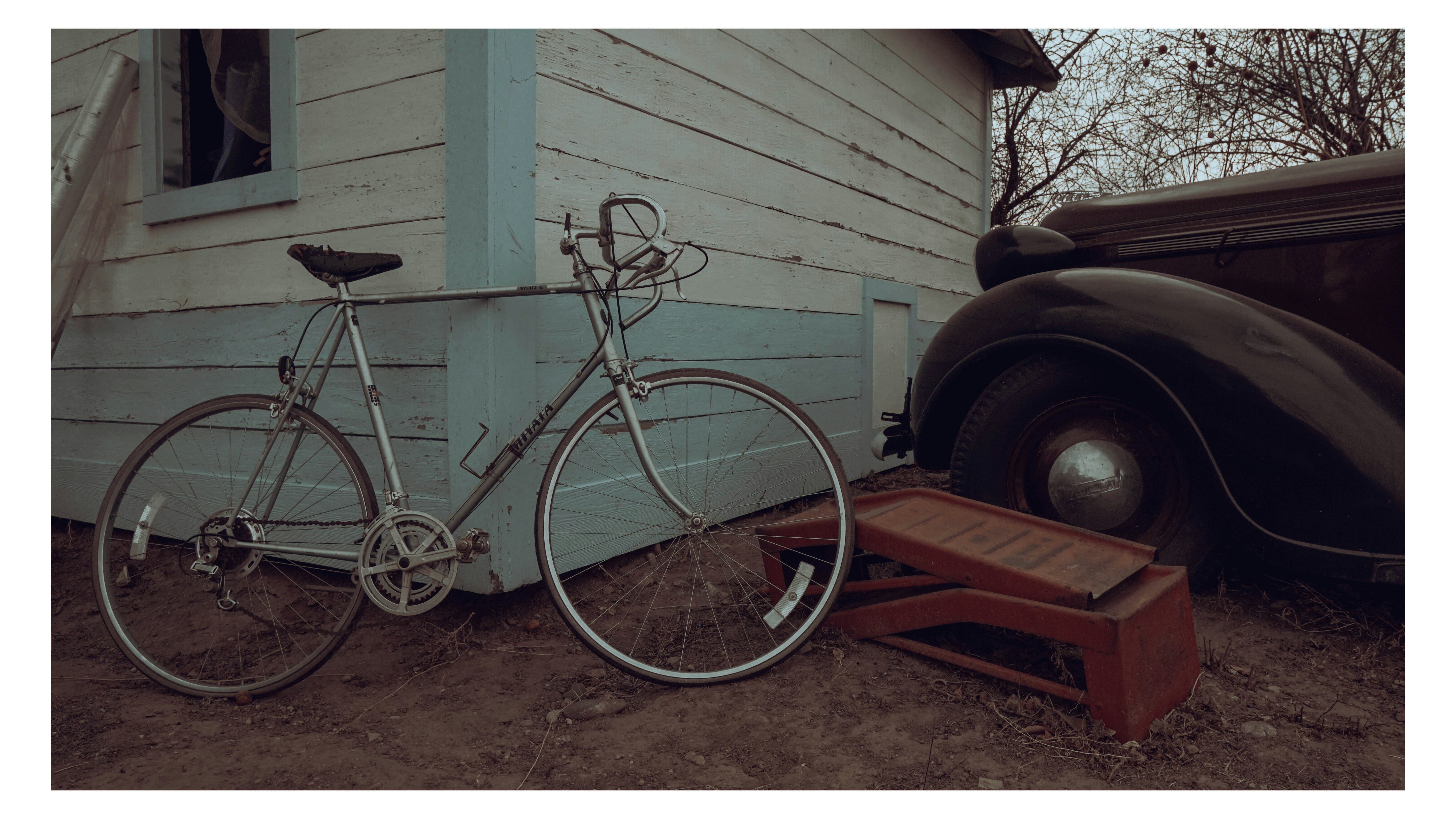 Dusty bicycle by a weathered shed with a rusted step stool