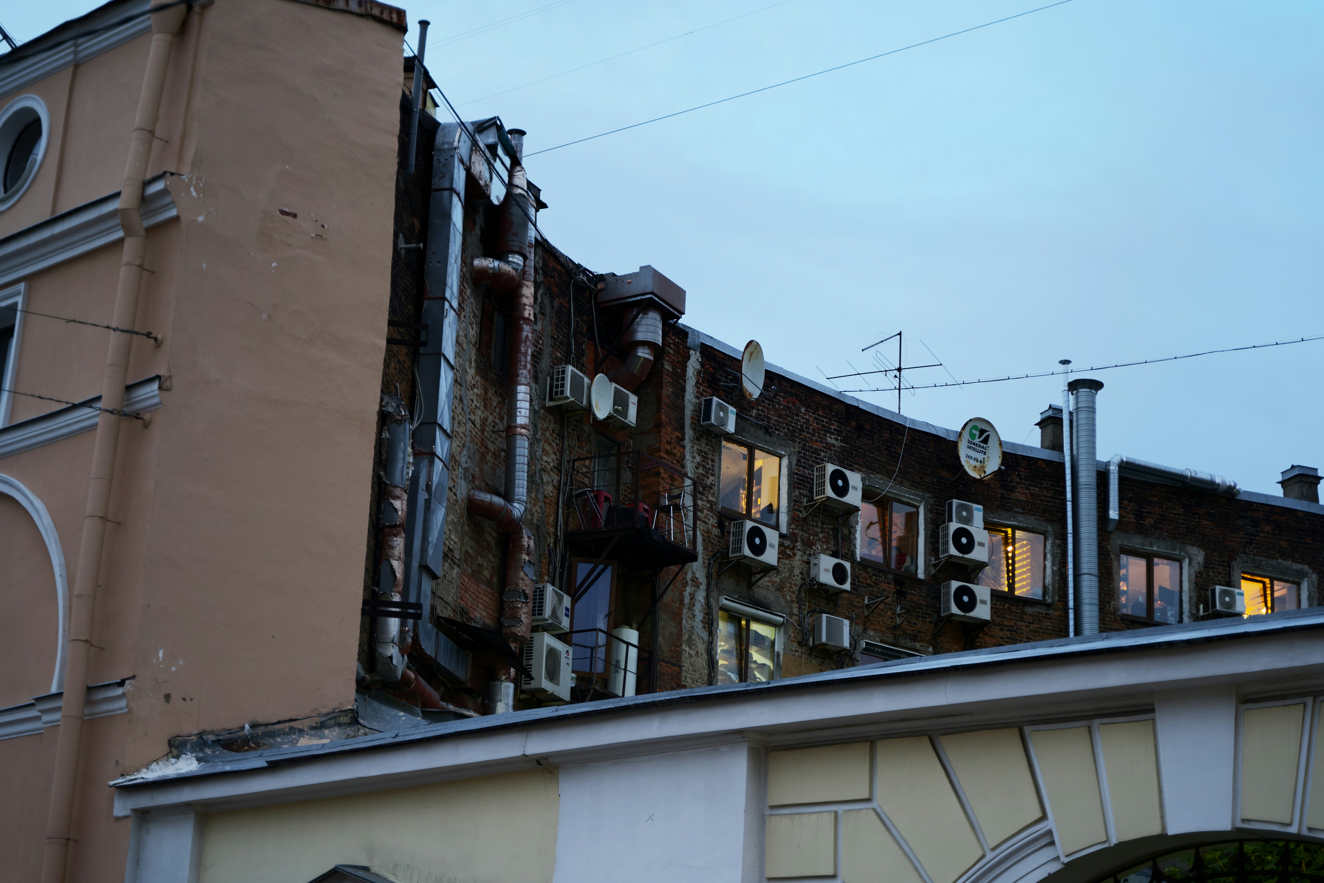 Weathered building exterior adorned with numerous air conditioning units, juxtaposed against a soft evening sky.