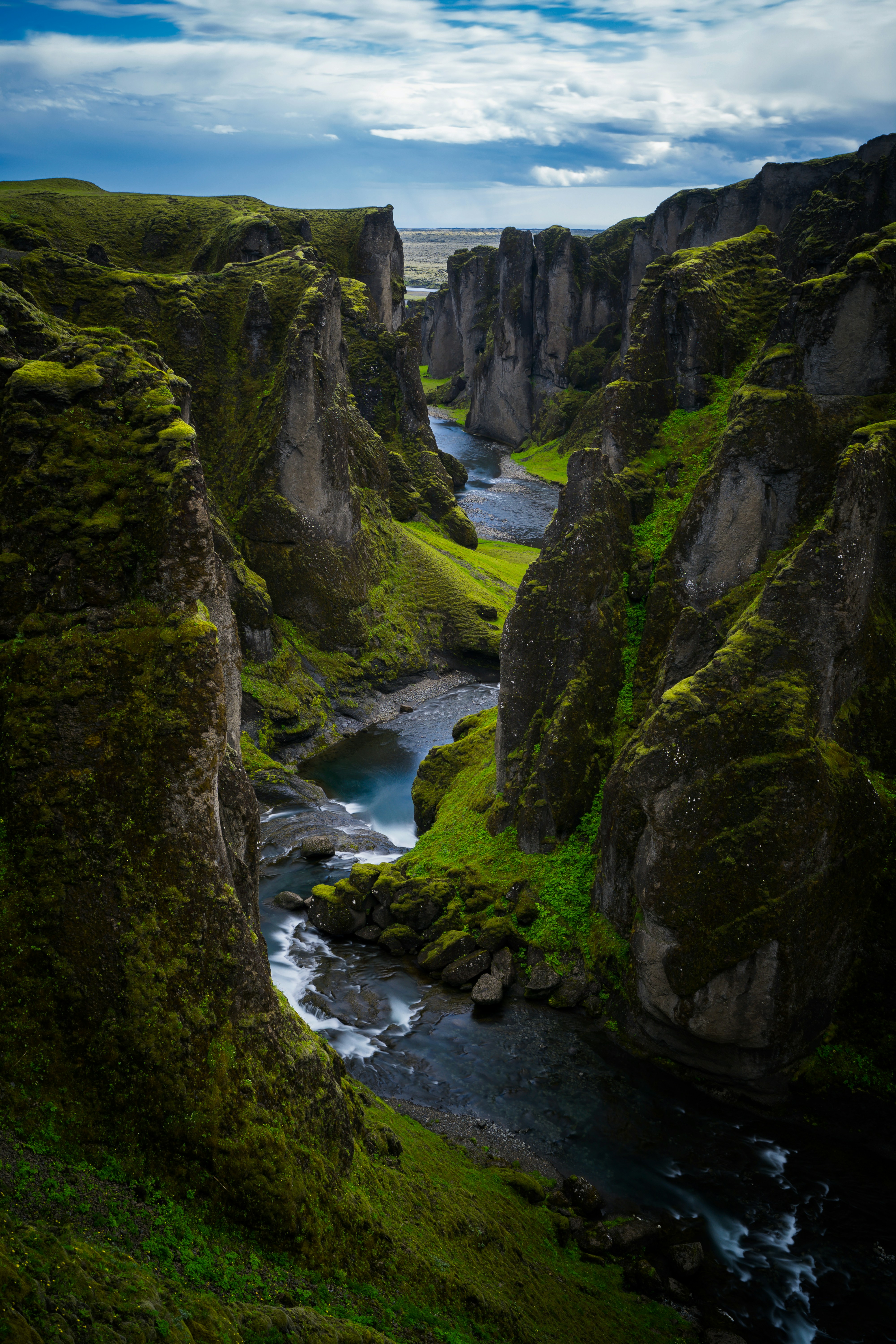 Lush green cliffs surround a winding river in a dramatic canyon, showcasing nature's artistry. The scene captures the interplay of light and shadow across the rugged landscape.