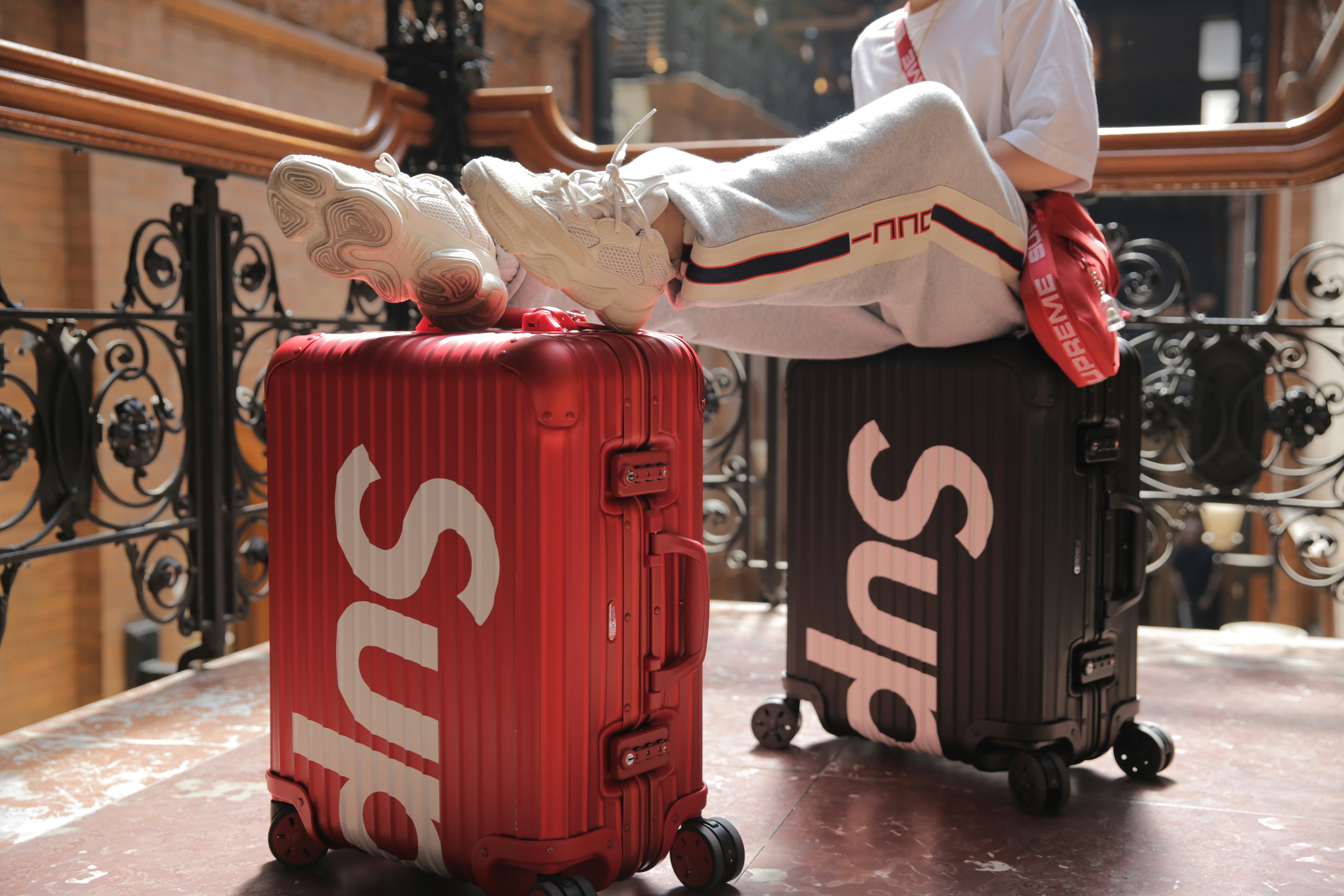 A person seated on two stylish suitcases, one red and one black, showcasing a modern travel aesthetic. The scene captures the intersection of fashion and functionality in urban travel.