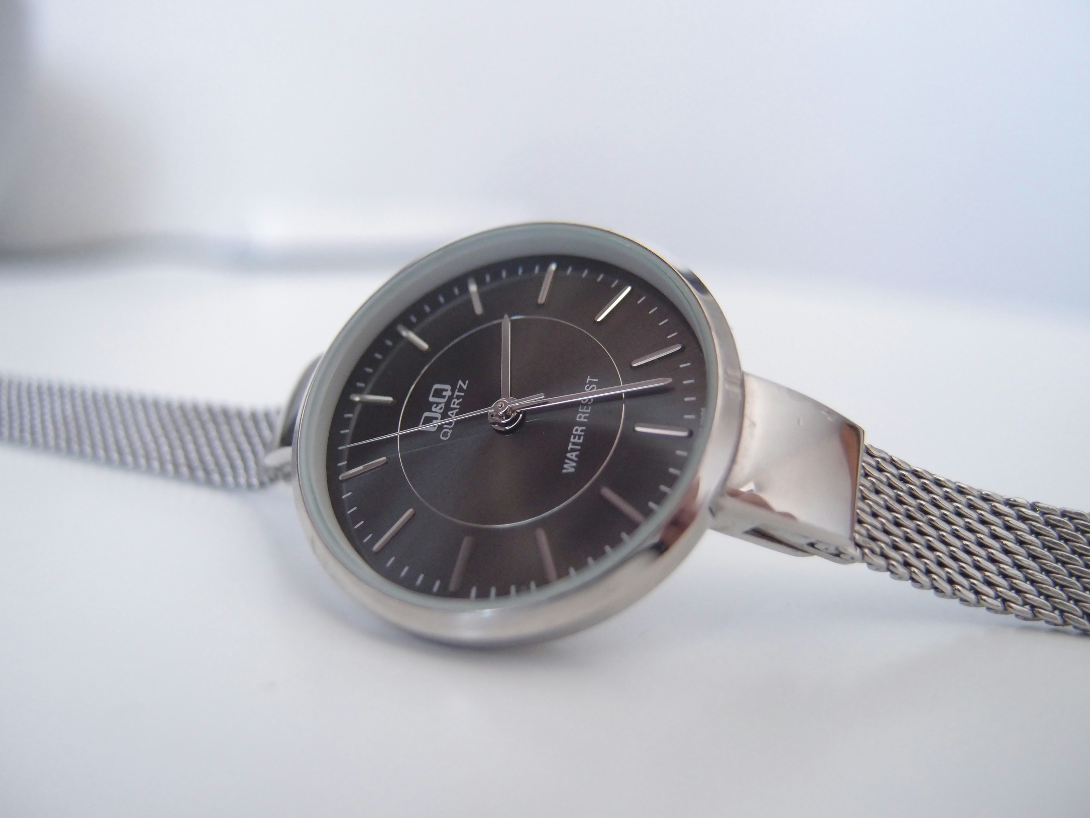 A sleek silver watch with a minimalist design, showcasing a dark dial and mesh band, highlighting its modern aesthetic.