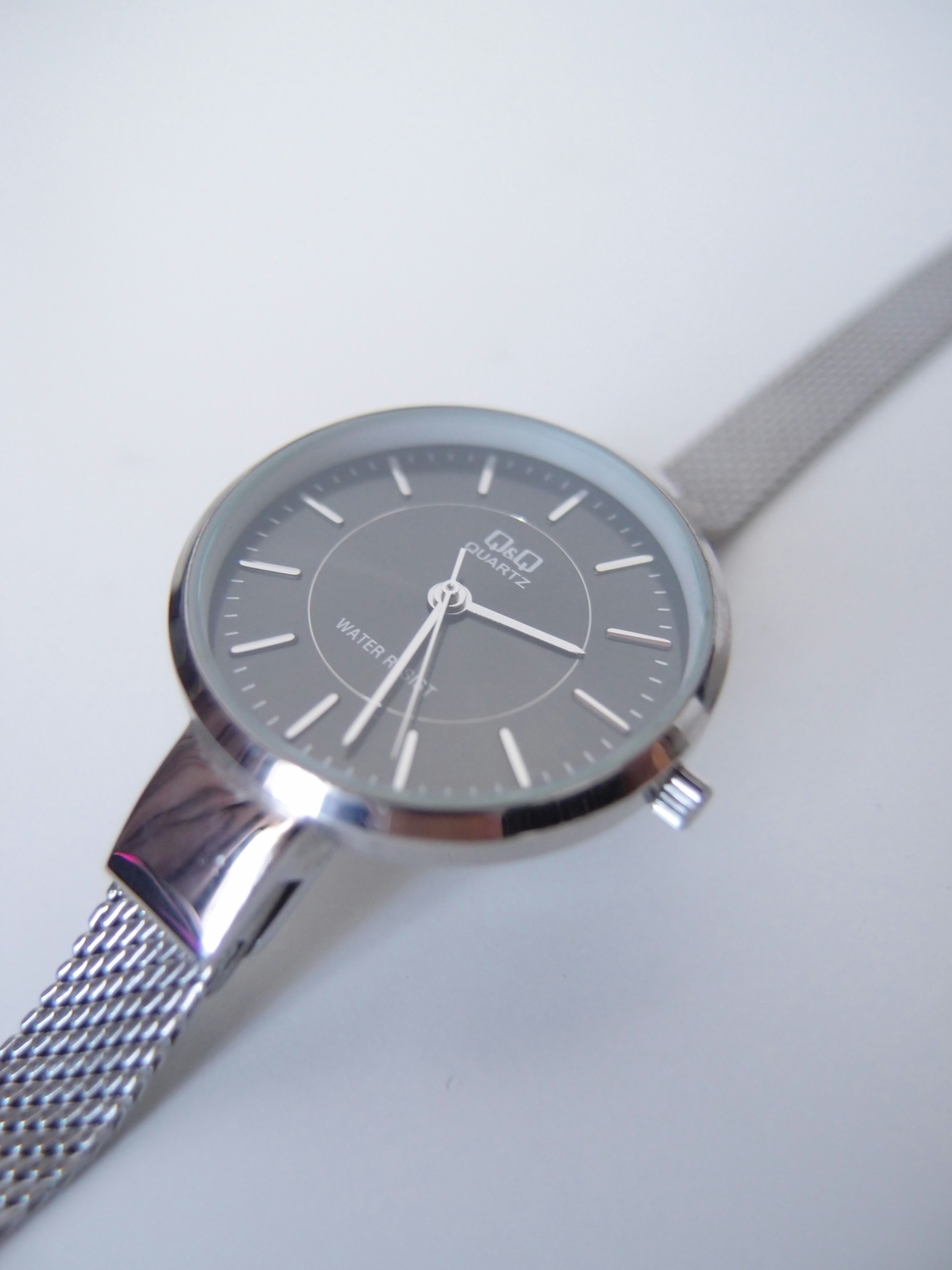 Close-up of a sleek quartz watch featuring a gray dial and metallic mesh strap. The watch showcases a modern aesthetic with understated sophistication.