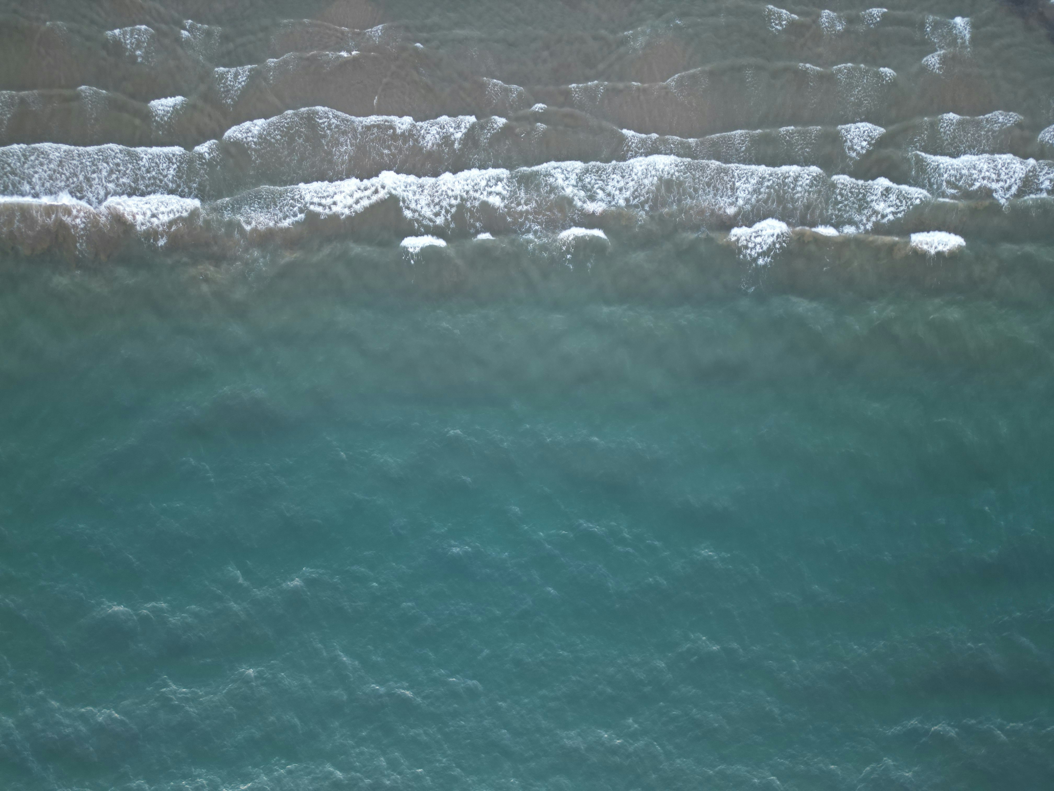 Aerial view of turquoise waves gently lapping against a sandy shoreline.