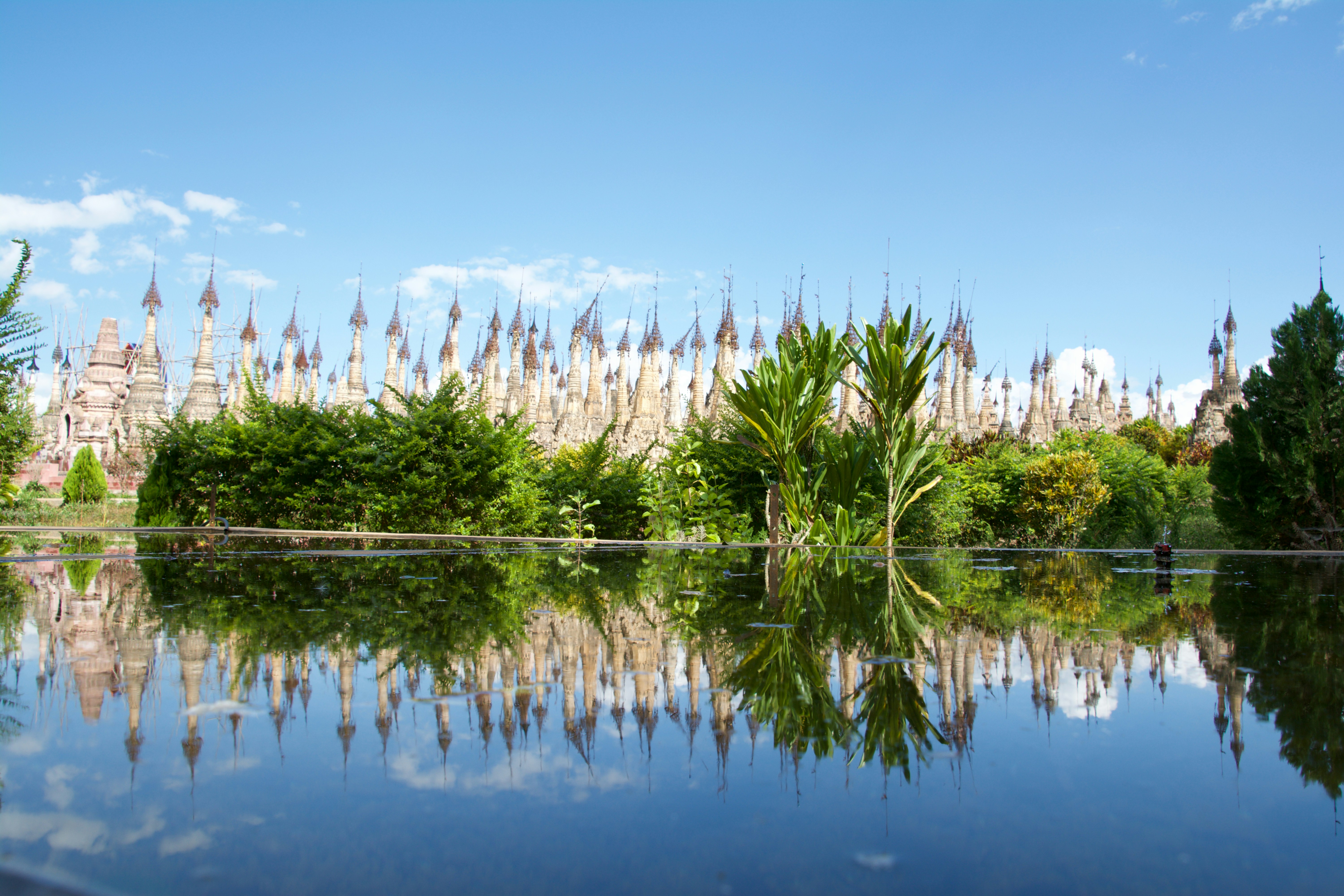A serene landscape featuring lush greenery and a clear reflection of ancient spires in a tranquil pool. The scene captures the harmony between nature and historical architecture.