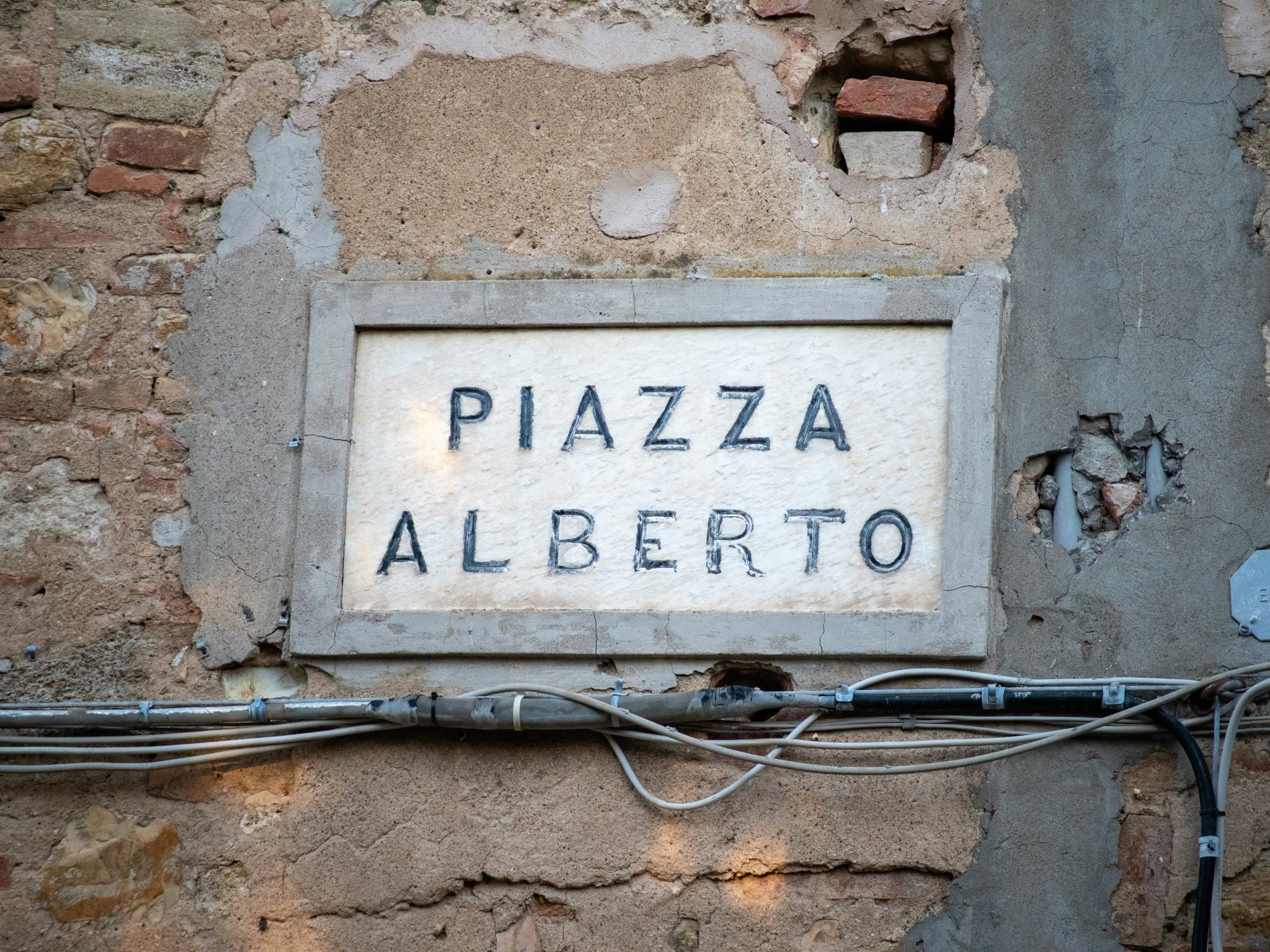 Weathered street sign displaying 'Piazza Alberto' against a rustic wall, showcasing the charm of old architecture.