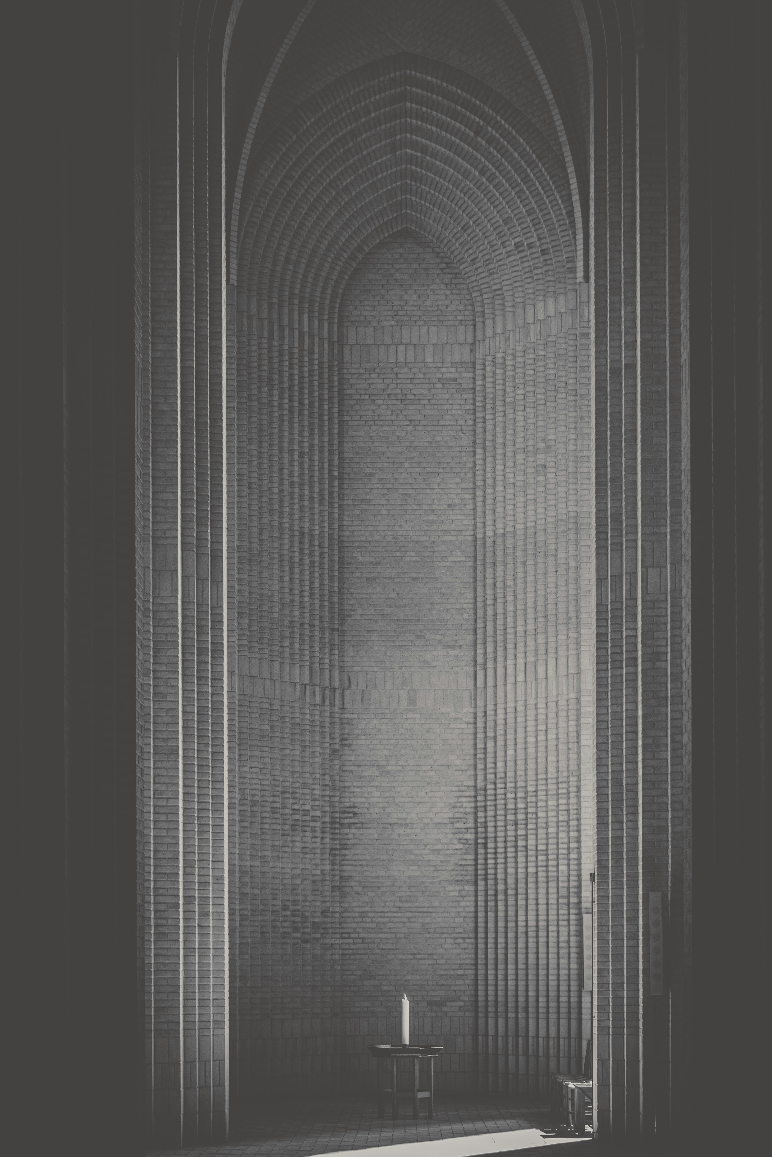 A solitary candle sits on a small table within a solemn Gothic nave. This grayscale photograph emphasizes architectural rhythm and quiet mood.