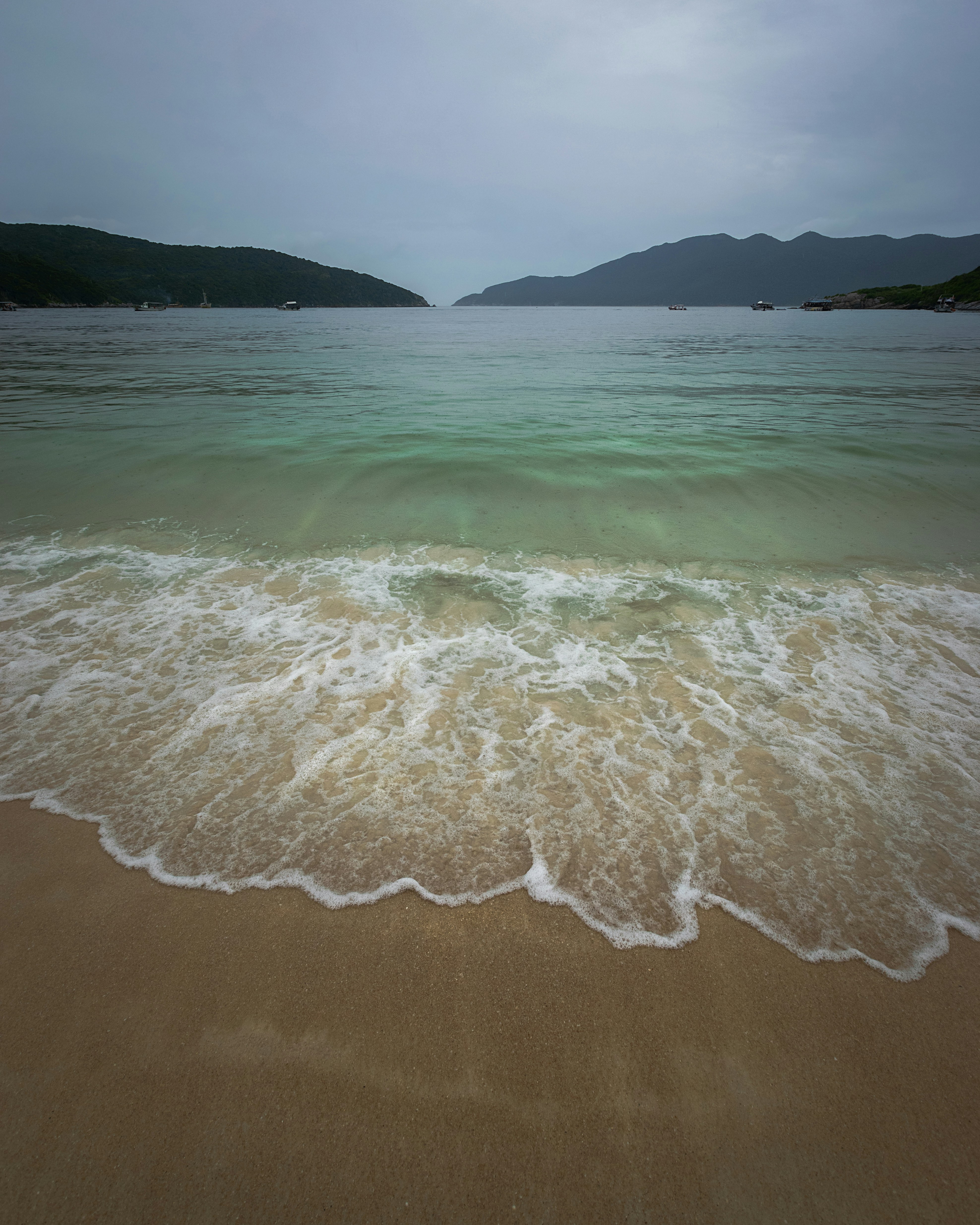 Muted Turquoise Shoreline: Foam Etching the Quiet Beach Under Overcast Skies