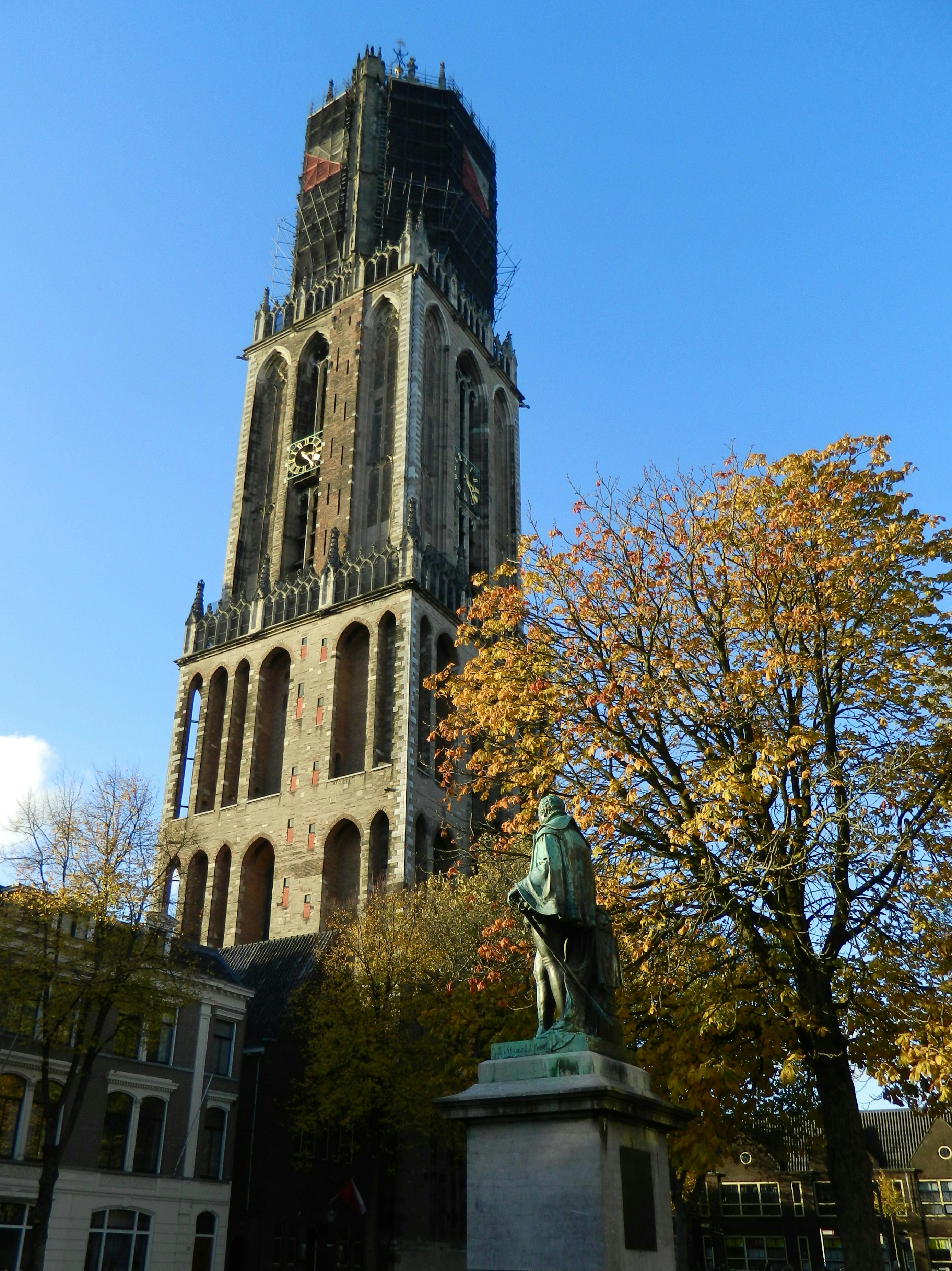 Historic bell tower framed by autumn foliage and a statue in the foreground. The structure showcases intricate architectural details.