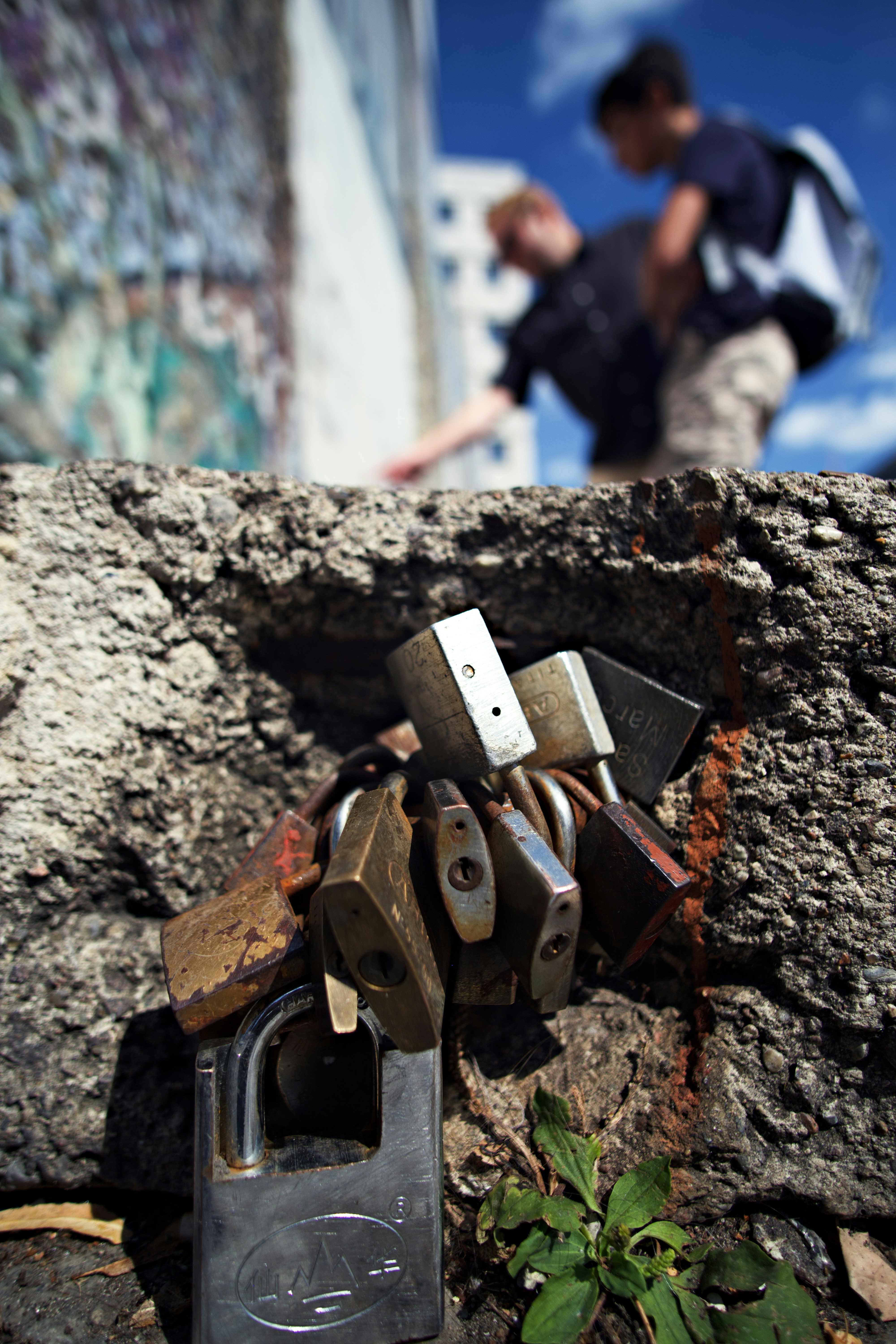 Locks in Concrete: A close-up of a cluster of padlocks with two blurred figures in the background