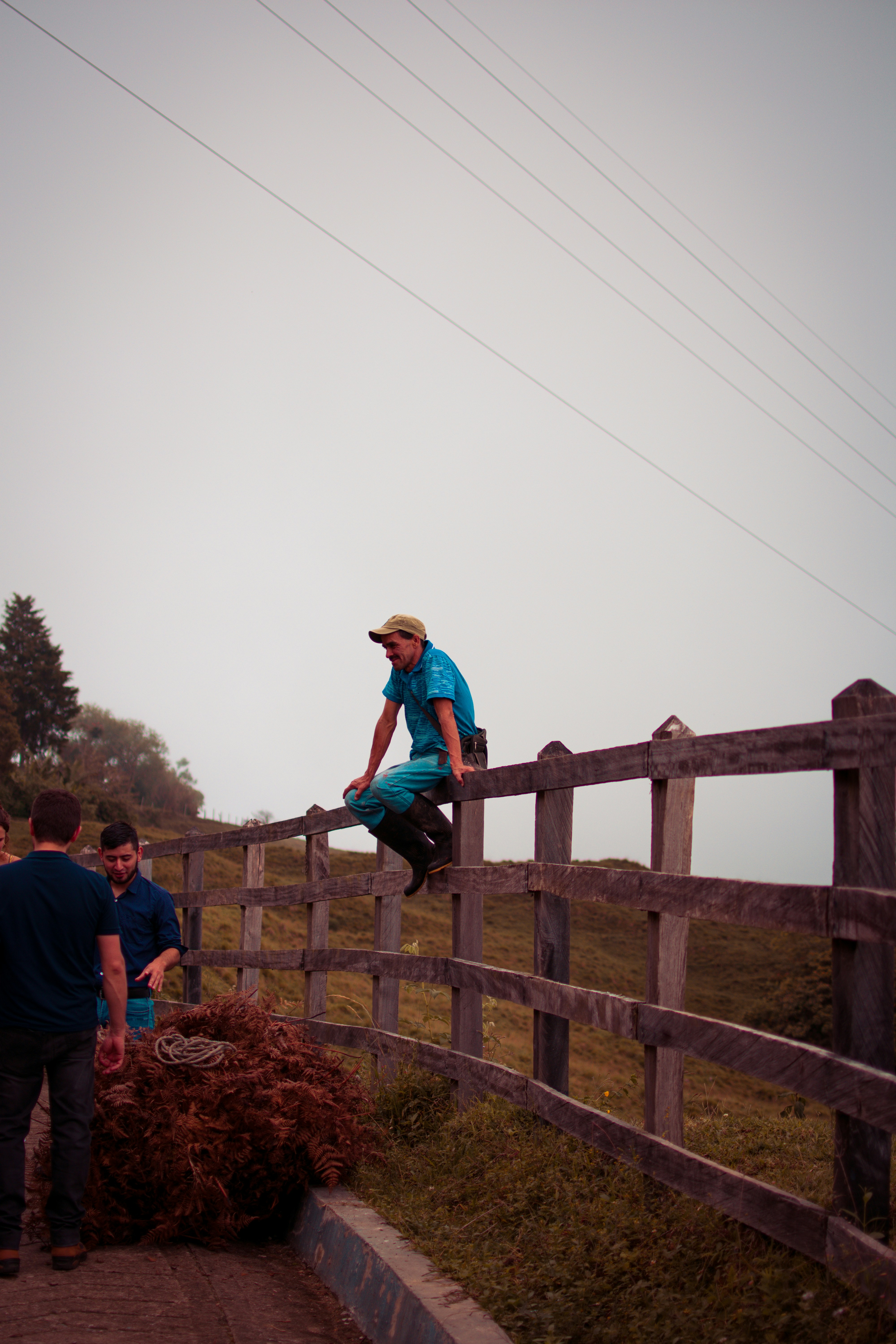 Man in turquoise climbs a weathered fence against a foggy hillside
