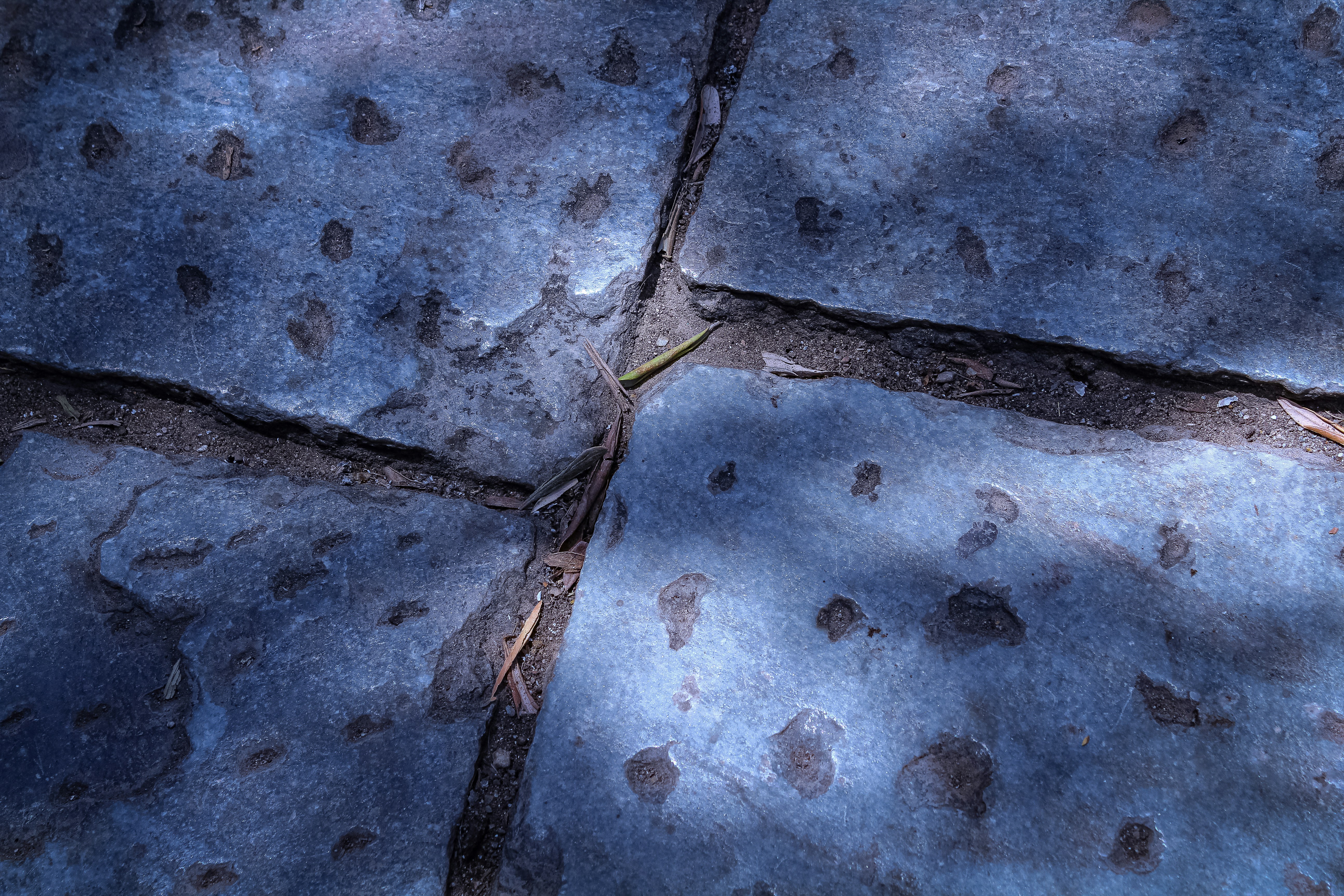 Close-up view of textured blue stone slabs interspersed with small cracks and patches of dirt, showcasing natural wear and age.
