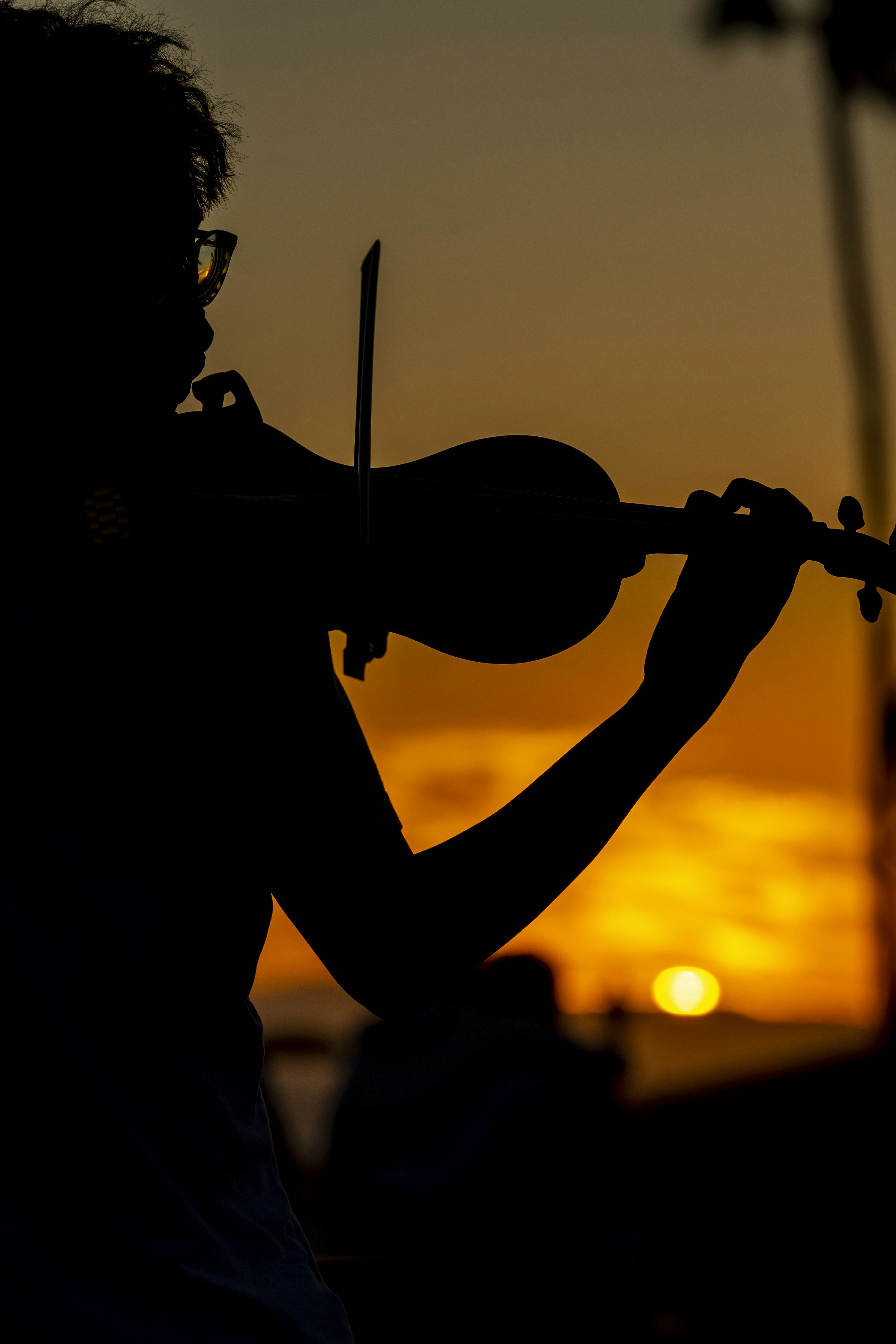 Silhouette of a musician playing the violin against a vibrant sunset backdrop, capturing a moment of artistic expression.