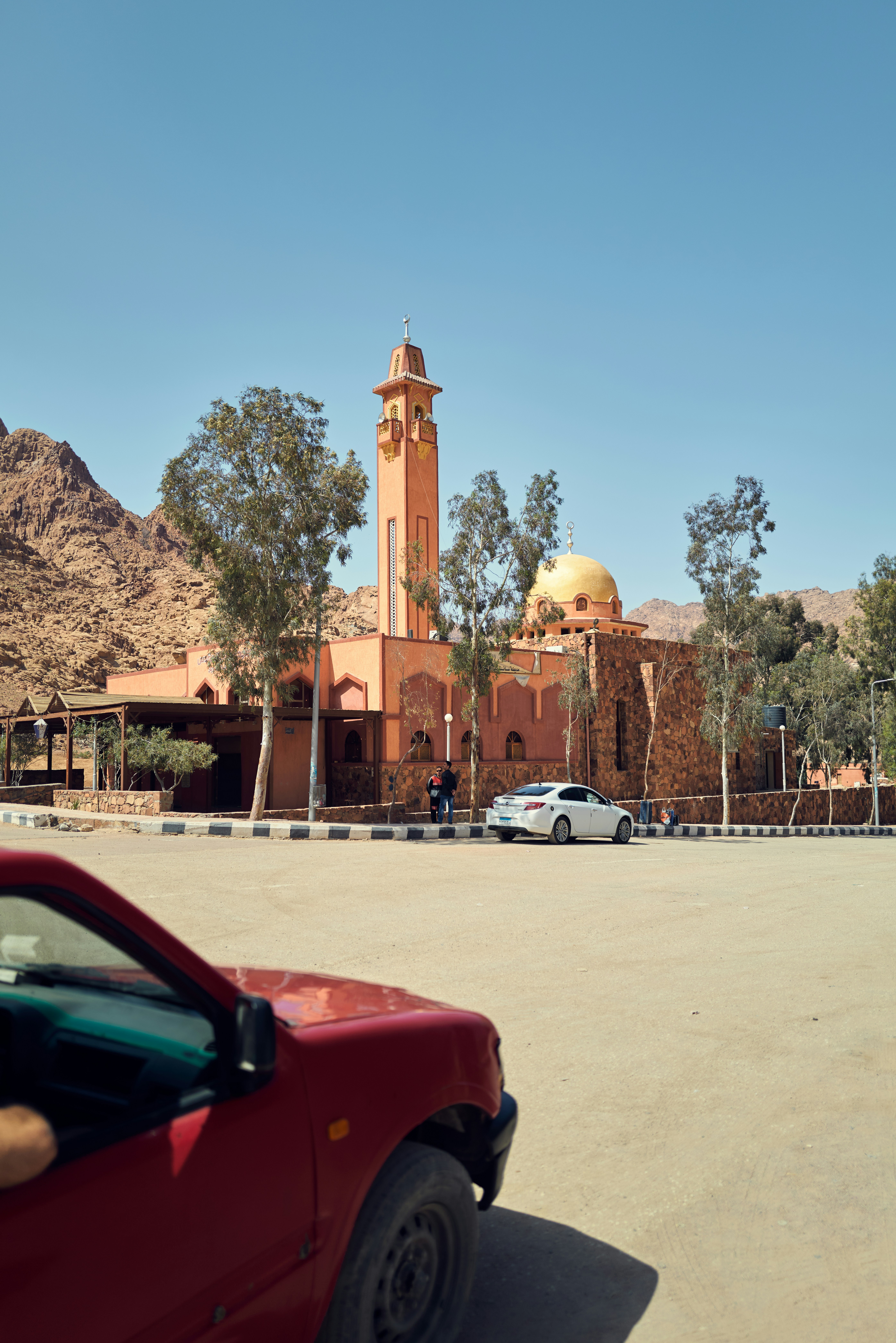 Desert Mosque Rising: Orange Walls, Golden Dome, and a Quiet Street Under a Clear Blue Sky