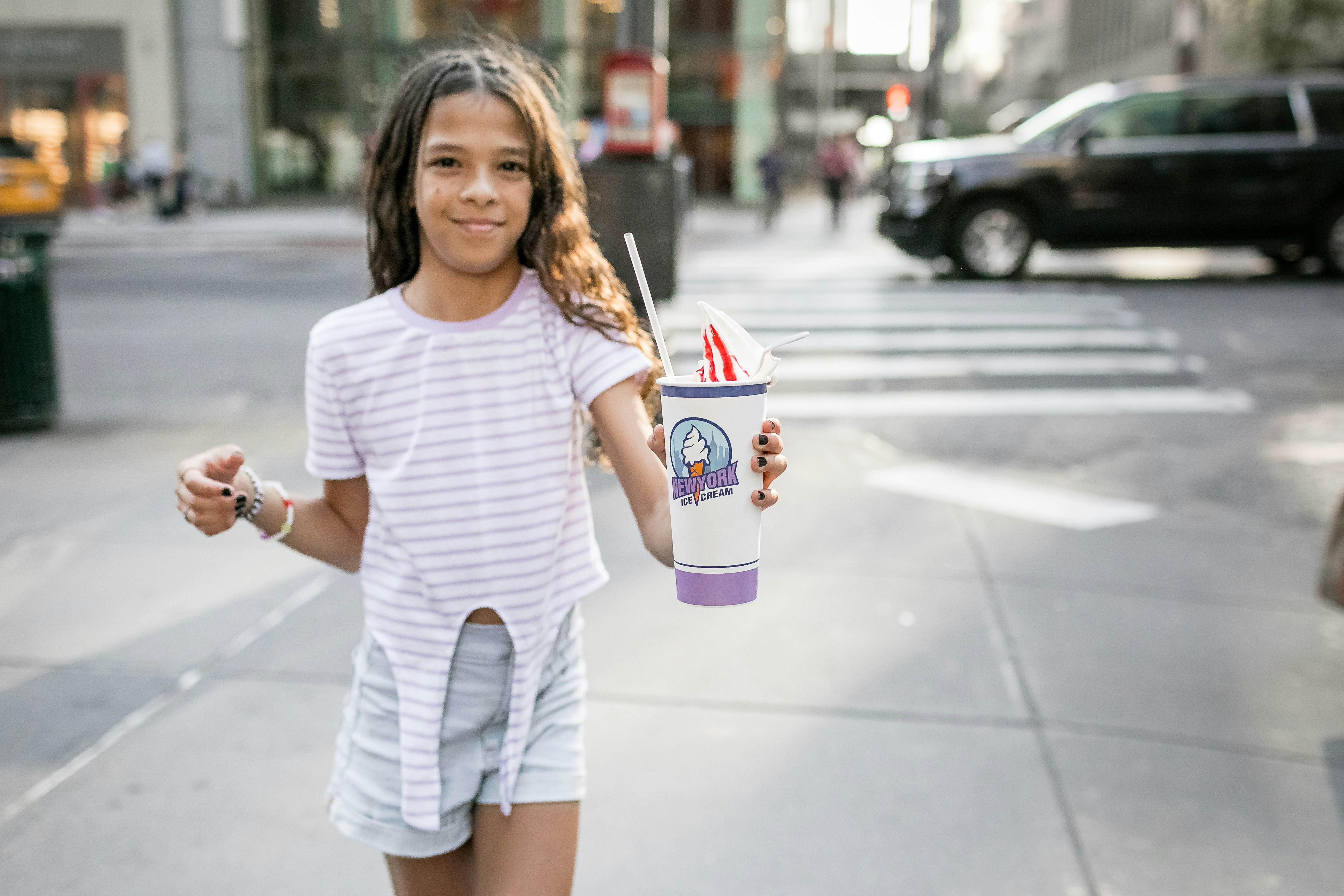 City Street Cheer: A Girl Extends a Cup in a Bright Afternoon