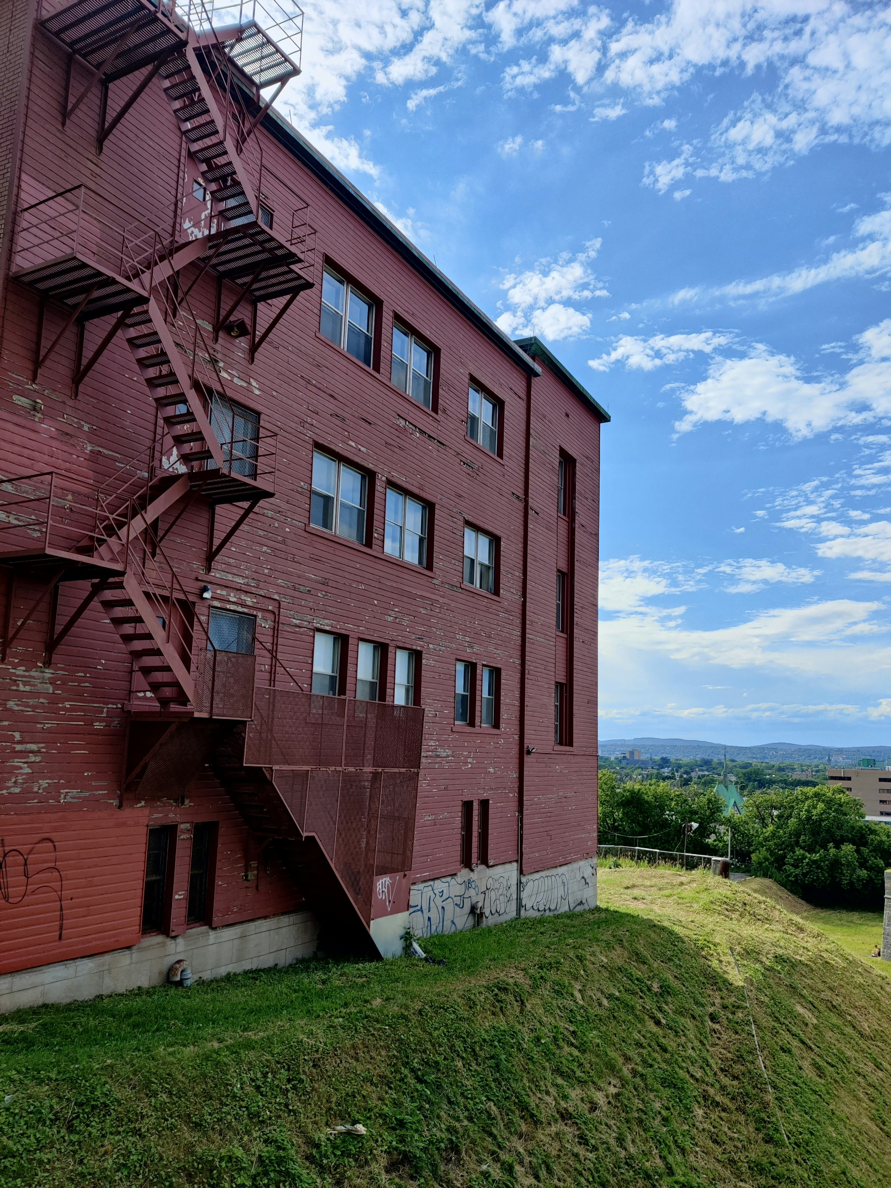 Red brick building featuring an exterior fire escape and a backdrop of a blue sky with scattered clouds.