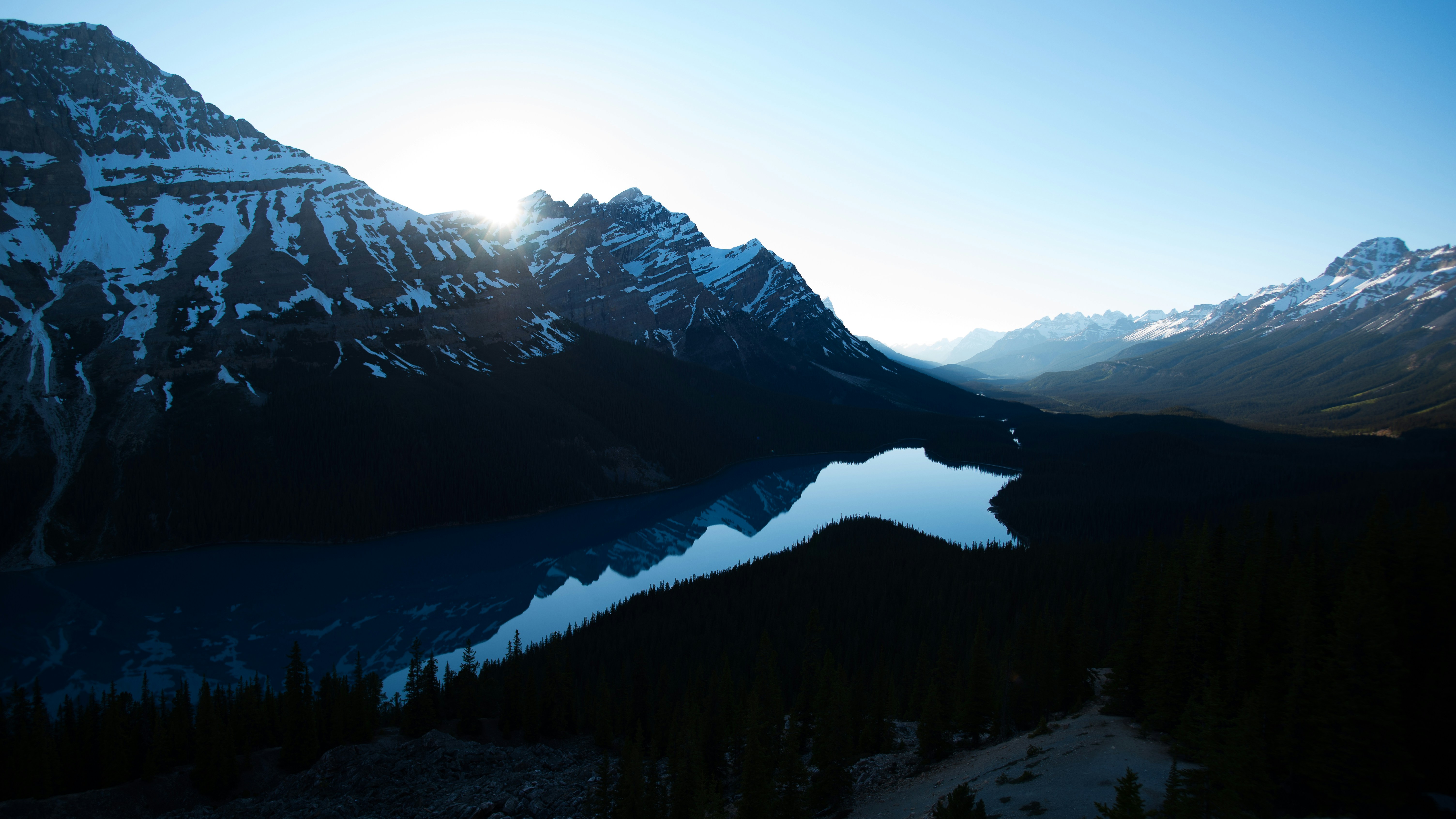 Snow-capped mountains reflecting in a serene lake under the early morning sky.