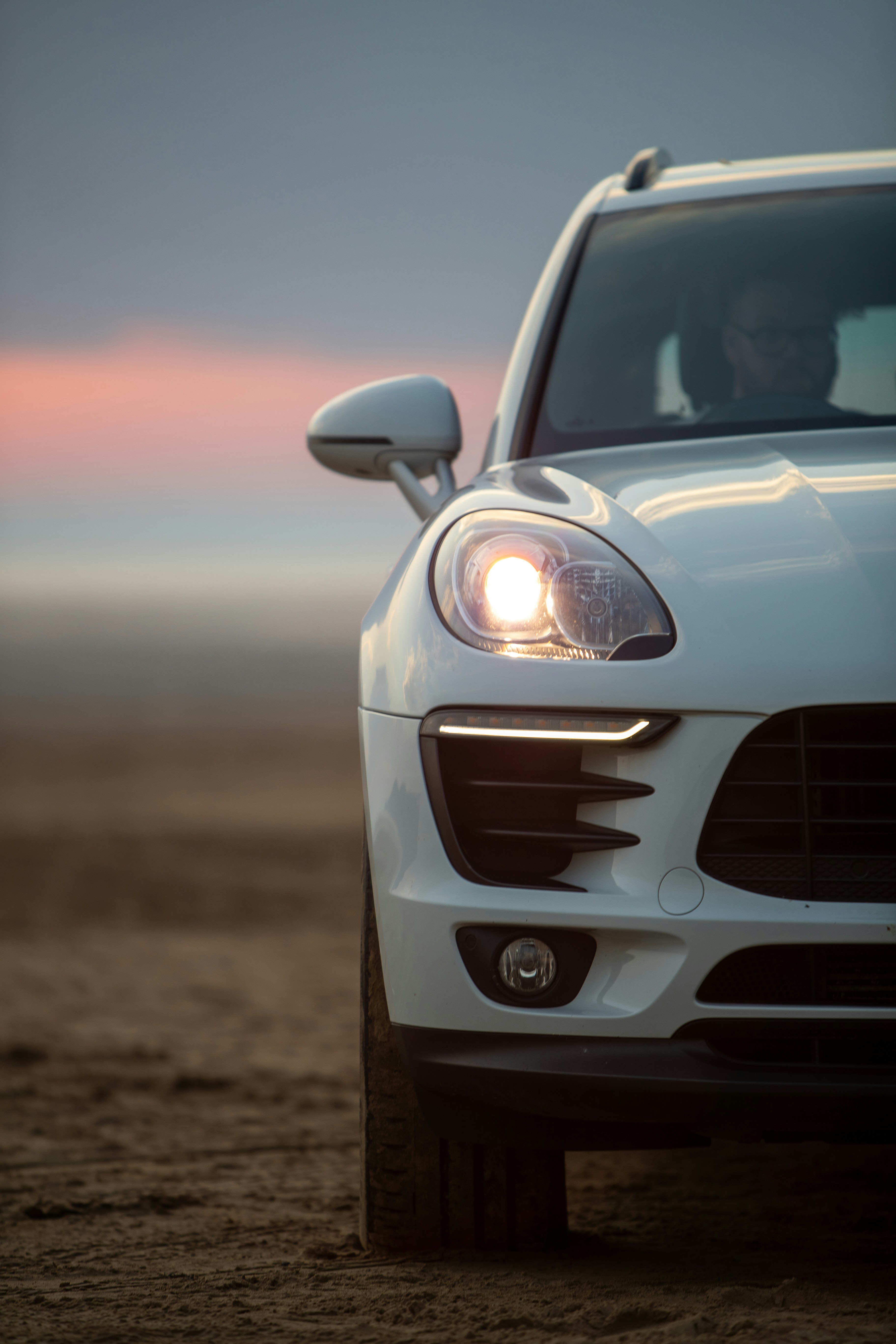 White SUV parked on a beach with dim headlights at dusk.