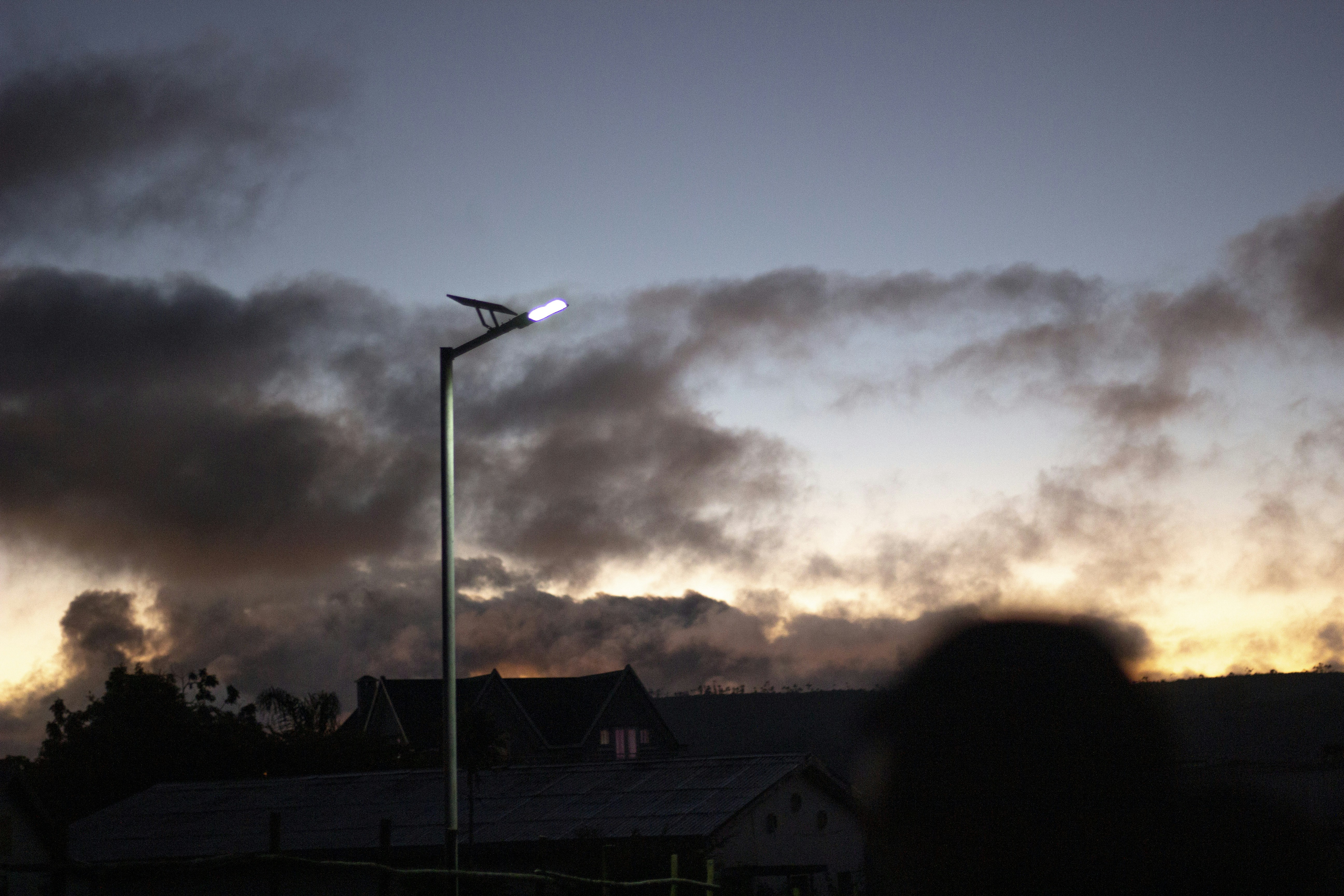 Streetlight glowing against a dramatic dusk sky with silhouetted houses.