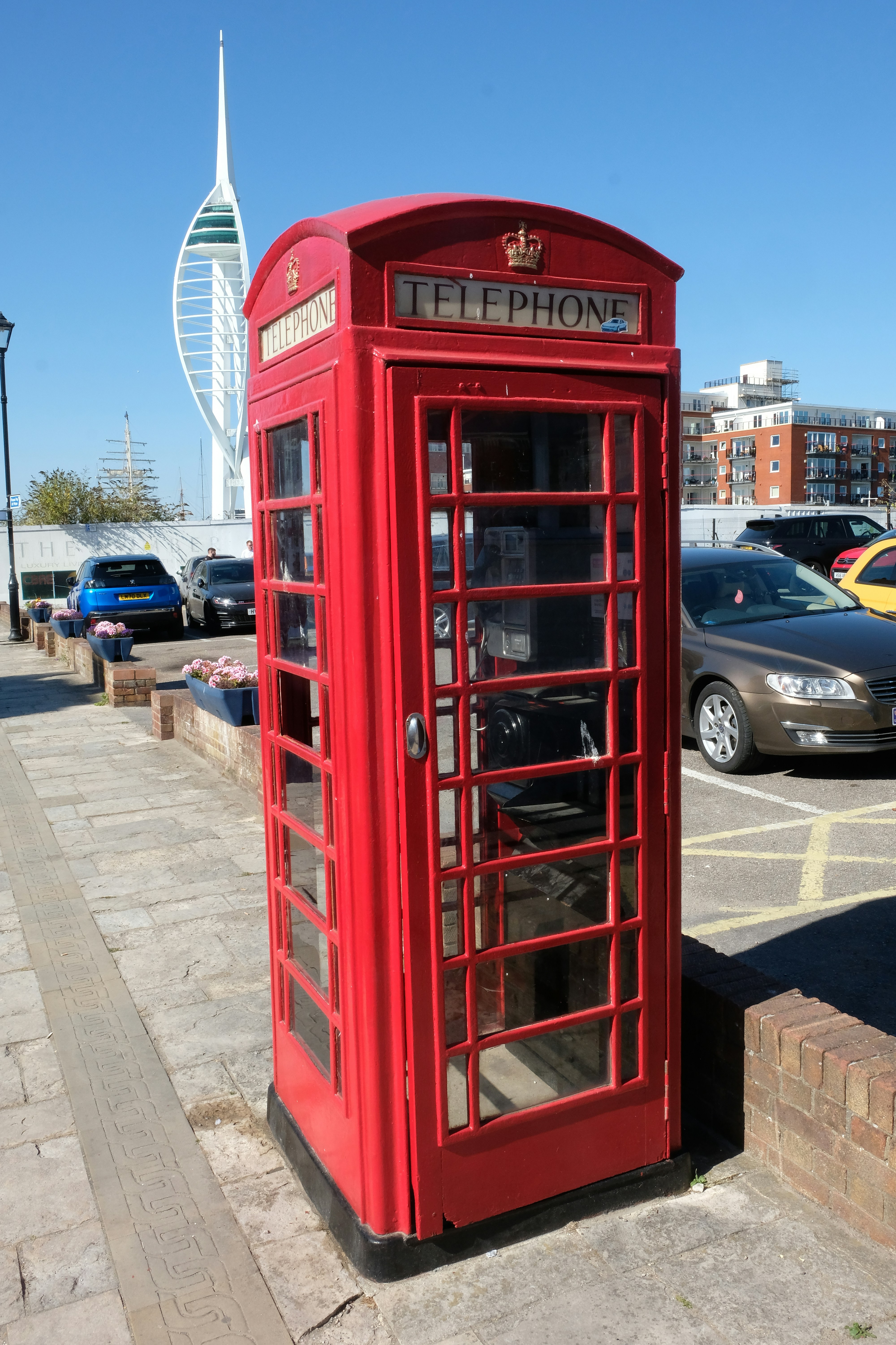 Scarlet Guardian: A Classic Red Telephone Kiosk Stands Against Modern Harbor Towers