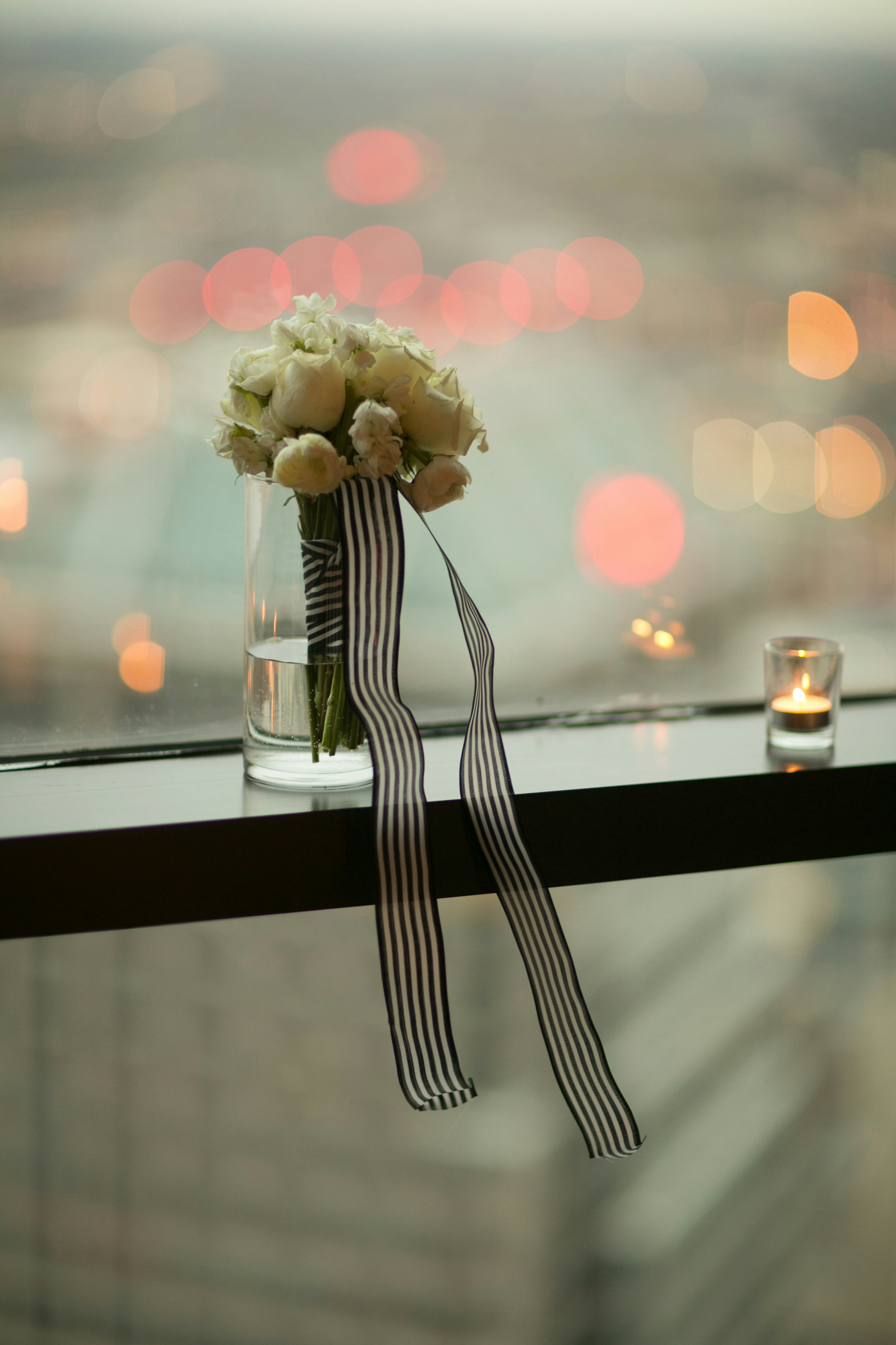 Ribbon-Wrapped White Bouquet on a Window Sill, City Lights Bloom in Bokeh