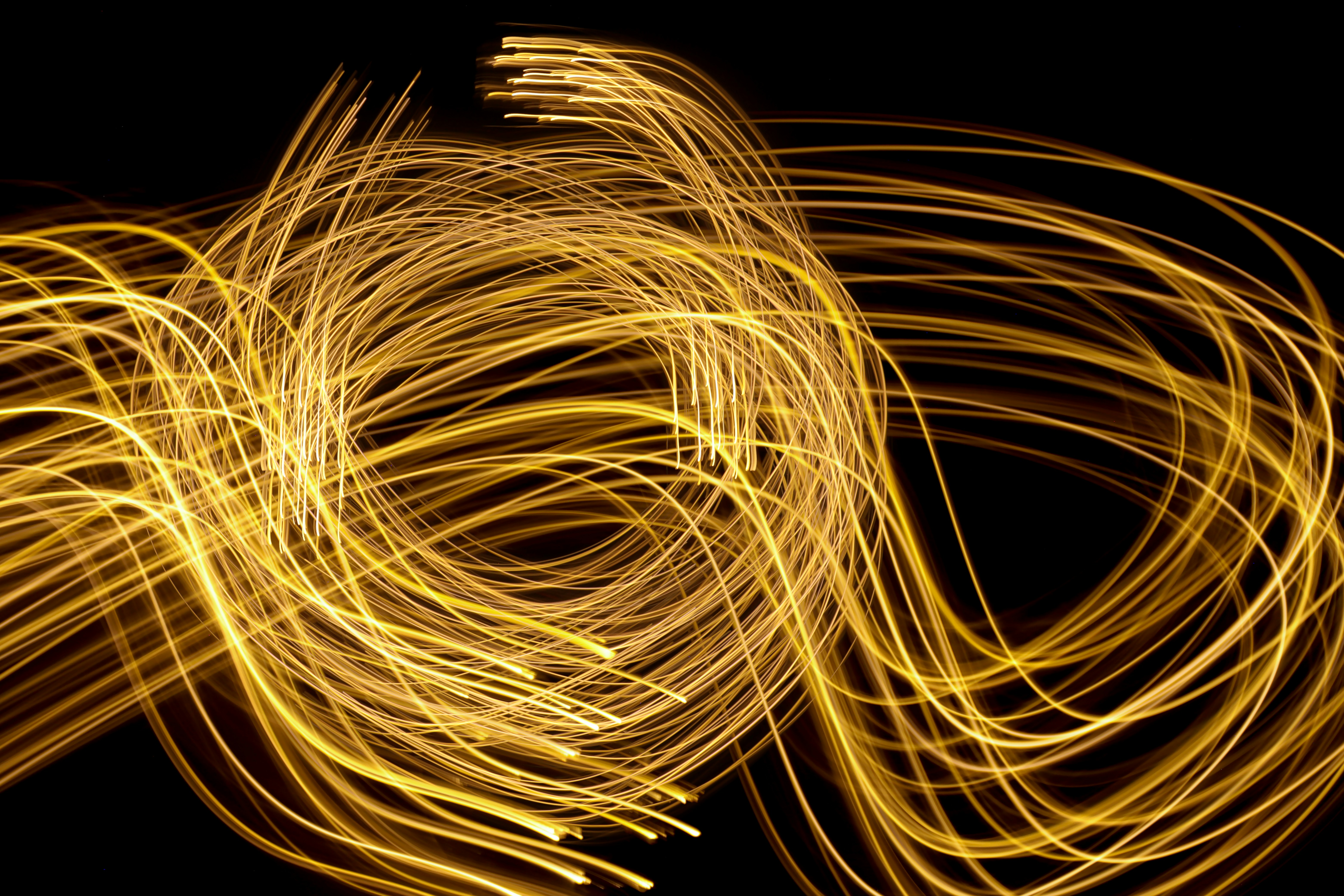 Swirling golden light trails create an abstract pattern against a dark backdrop, conveying a sense of motion and energy.
