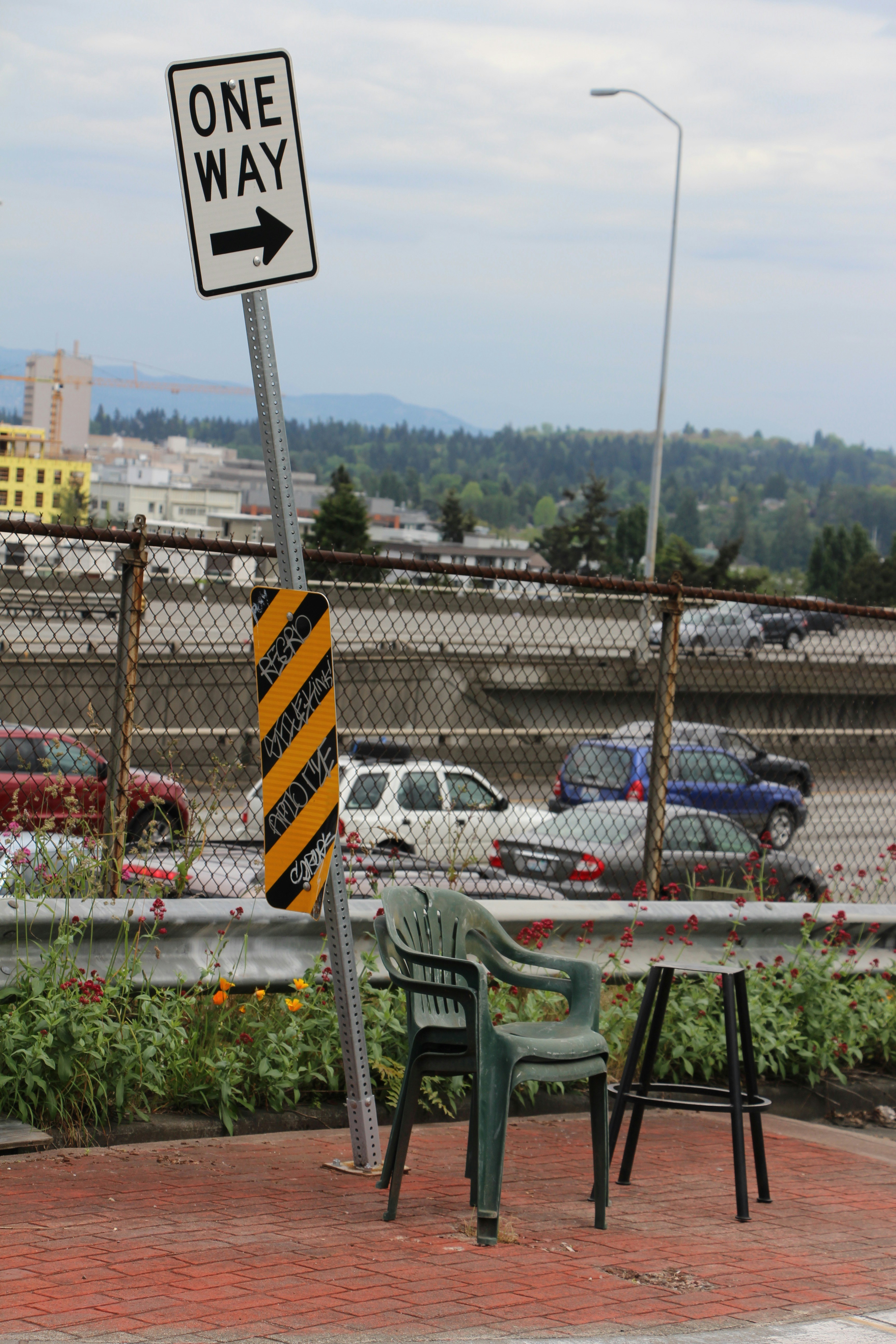 One Way Lean: A Leaning Sign Framed by Fence and Flowers