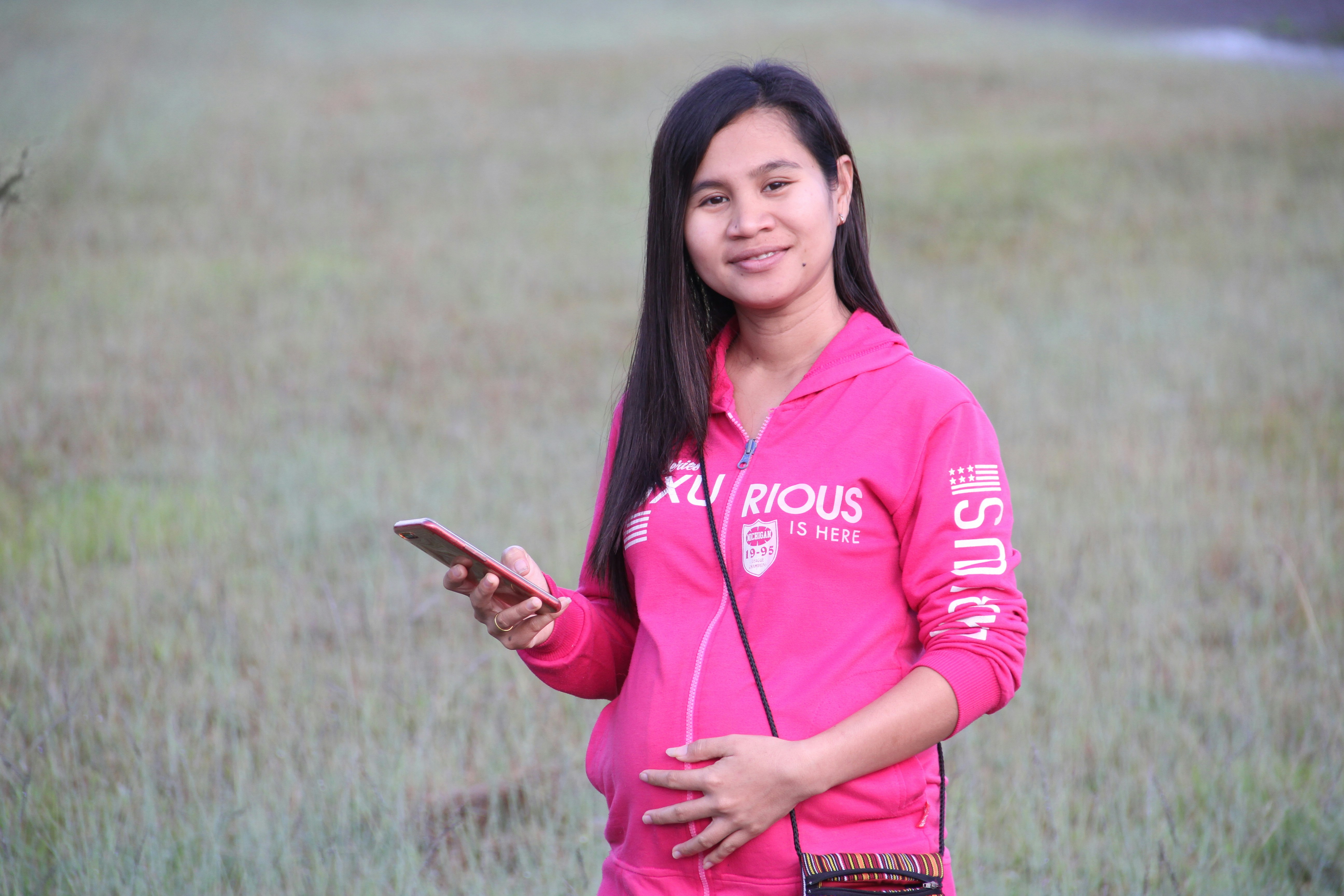Field Portrait of Expectation: A Pregnant Woman in a Pink Hoodie with a Smartphone
