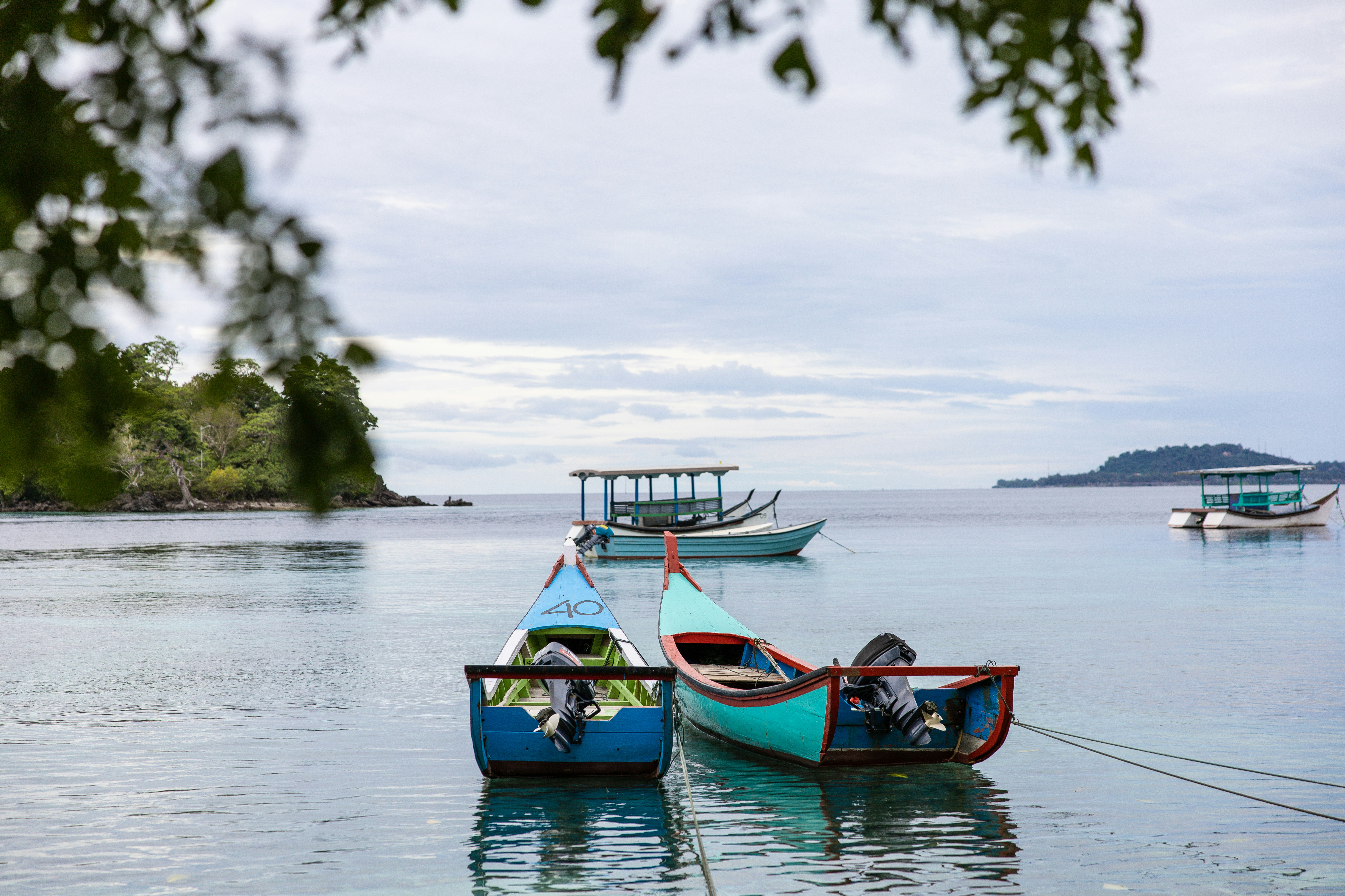 Colorful boats anchored on a calm sea with distant islands under an overcast sky.