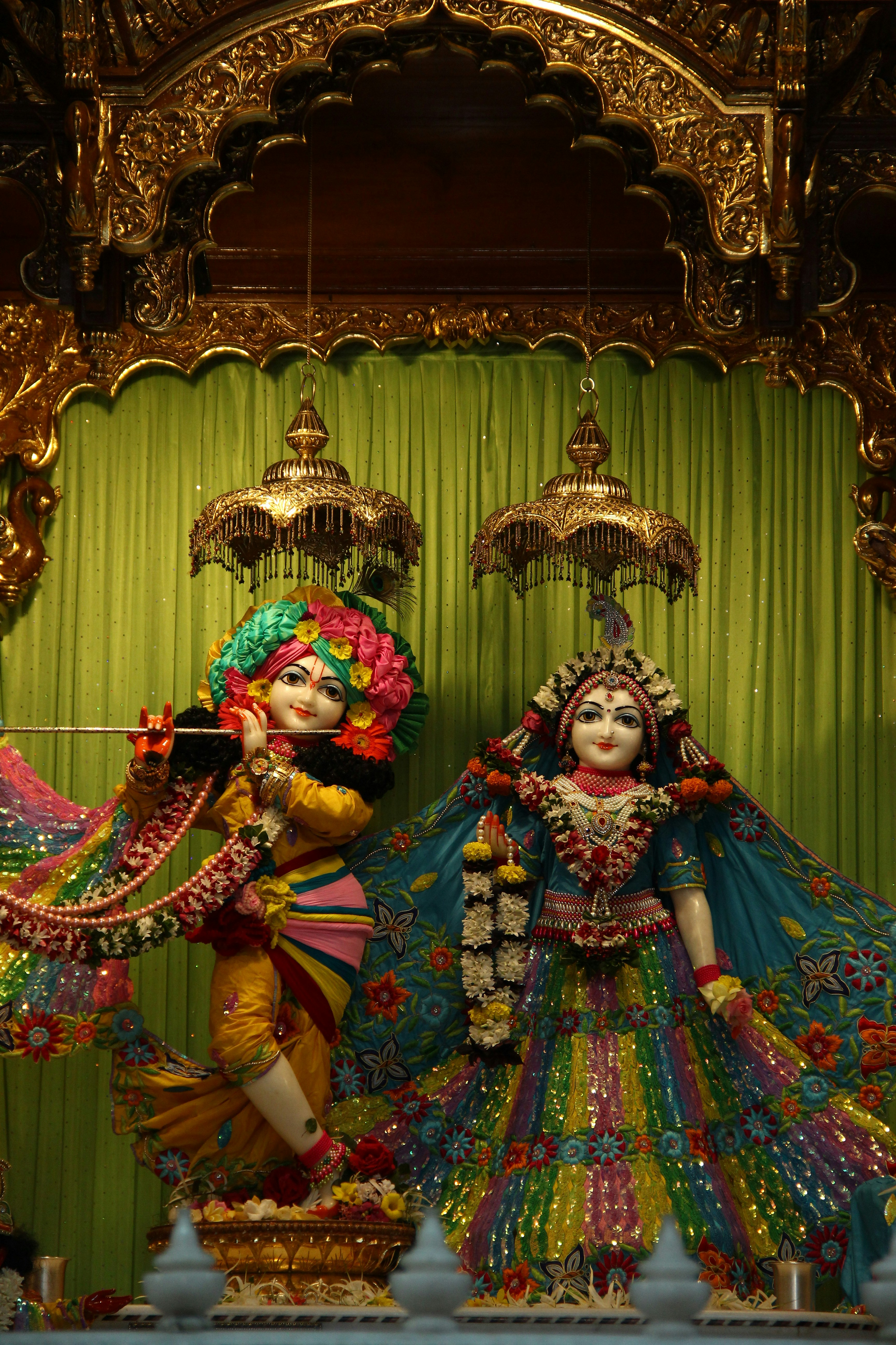 Intricately adorned statues of deities under ornate canopies with vibrant floral decorations and golden accents.