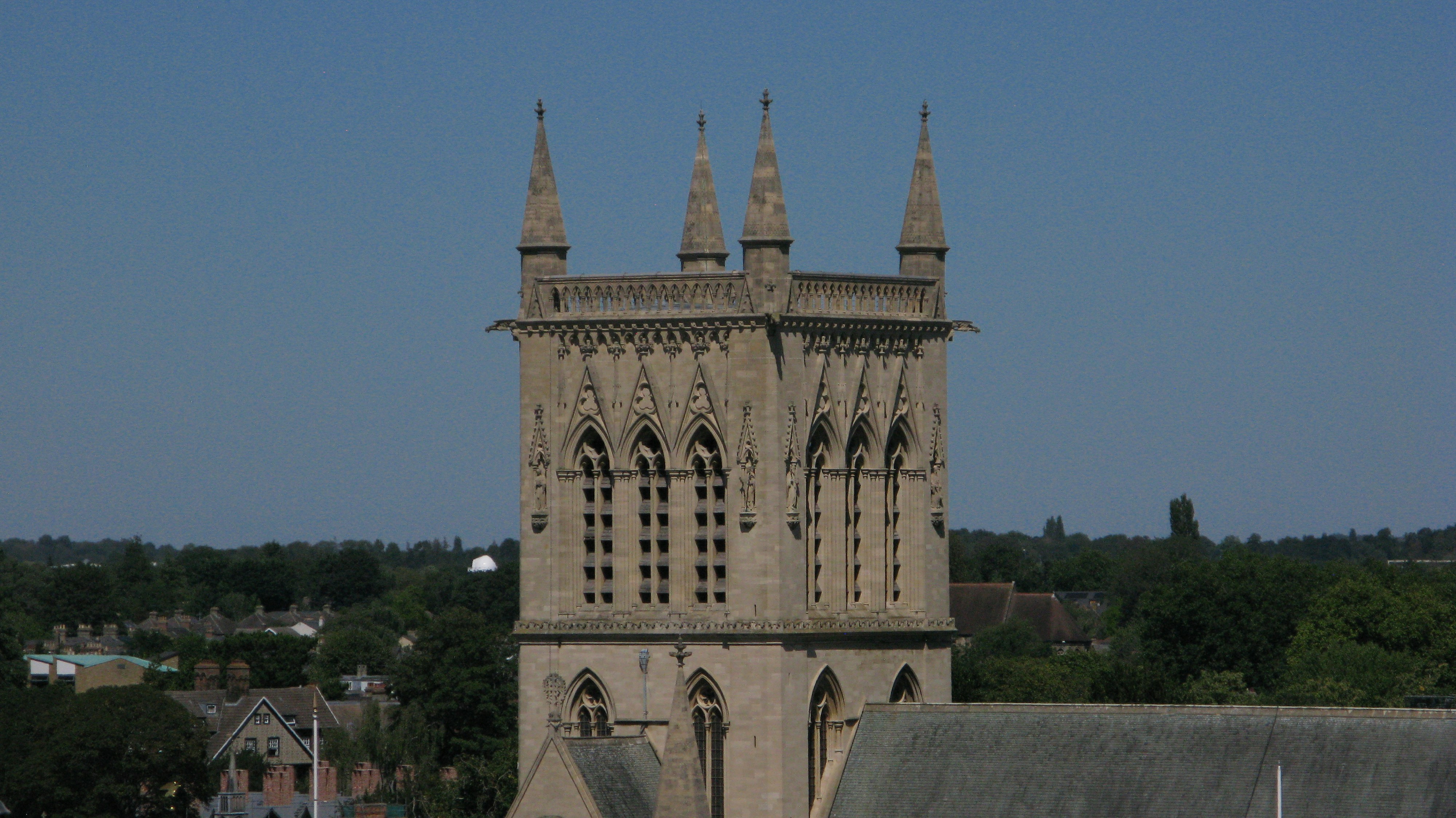 Architectural tower with intricate stonework rising against a clear blue sky, surrounded by lush greenery.