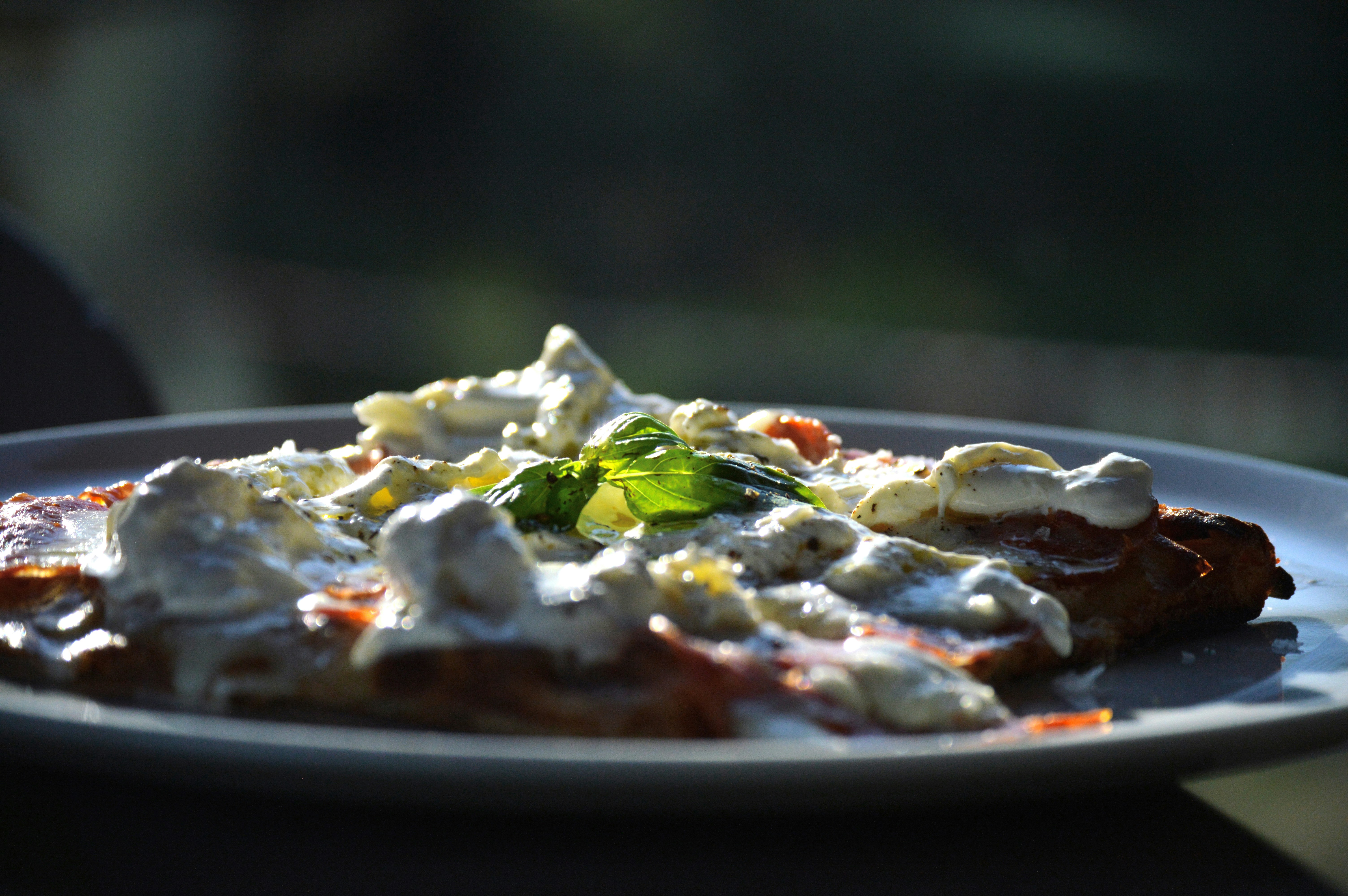 Delicious pizza topped with creamy sauce and fresh herbs, elegantly presented on a white plate. The warm lighting enhances the dish's appeal.