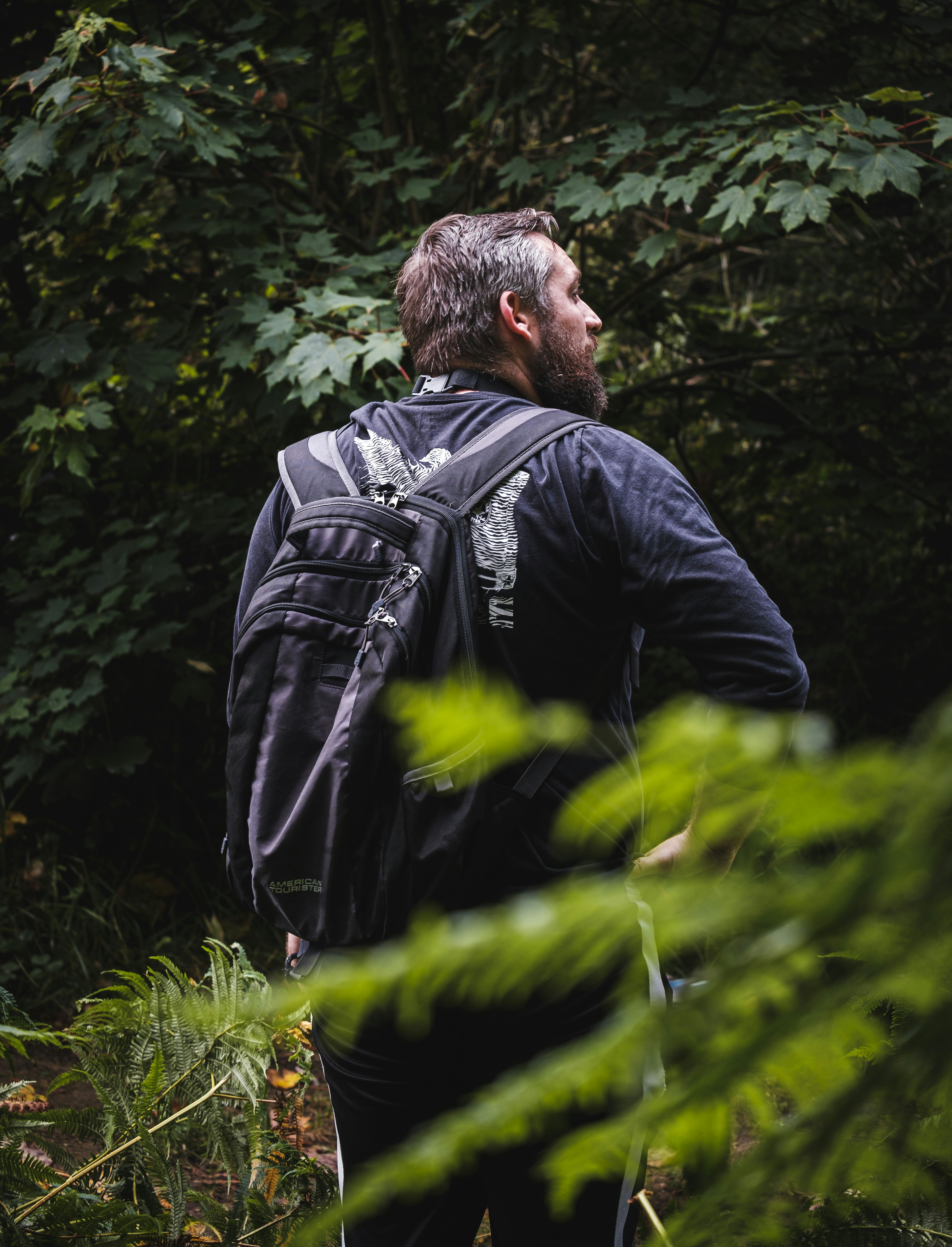 A hiker pauses amidst lush greenery, contemplating the path ahead with a backpack and a serene expression.