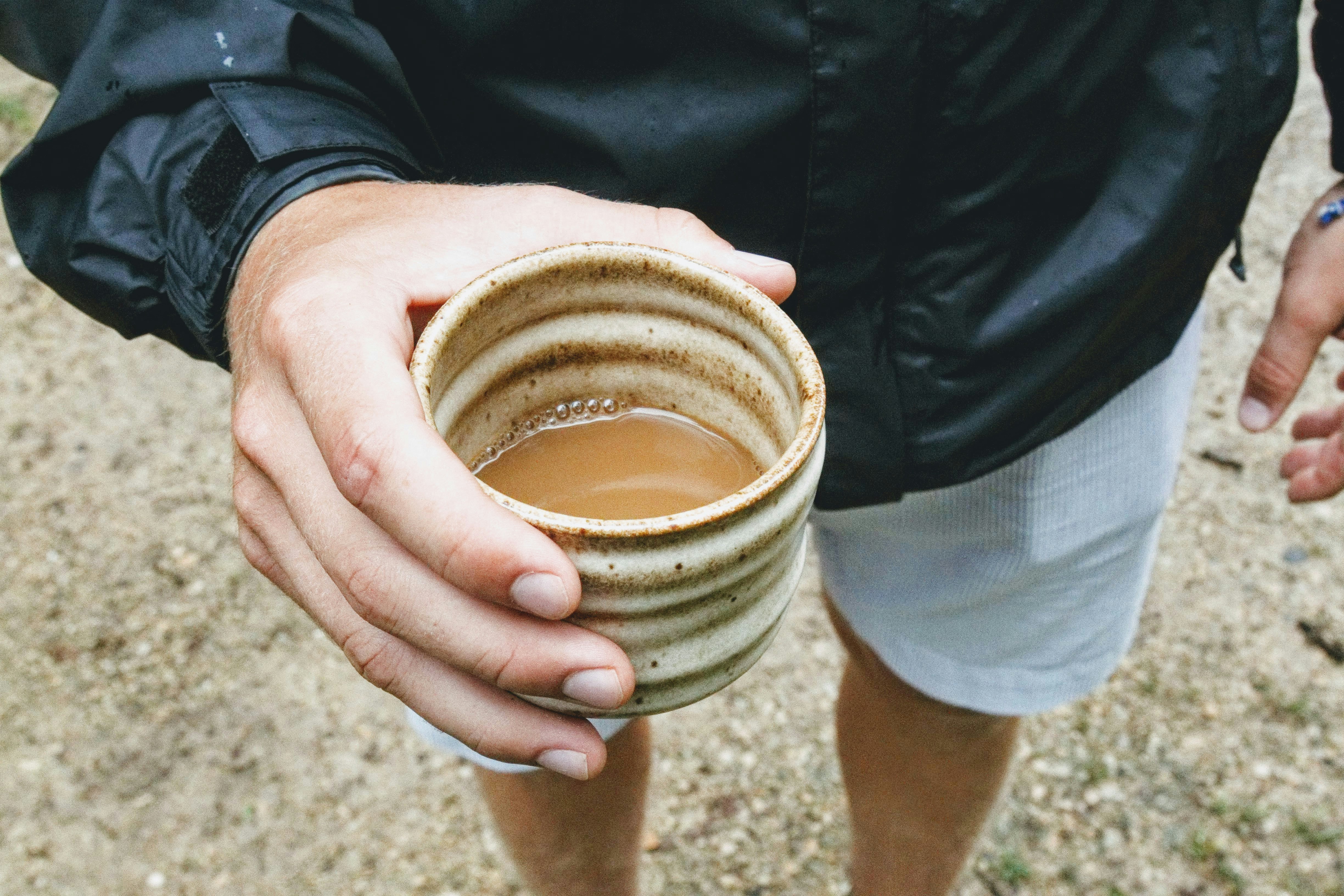 Earth-Tone Ceramic Cup in Hand: A Quiet Moment on Gravel