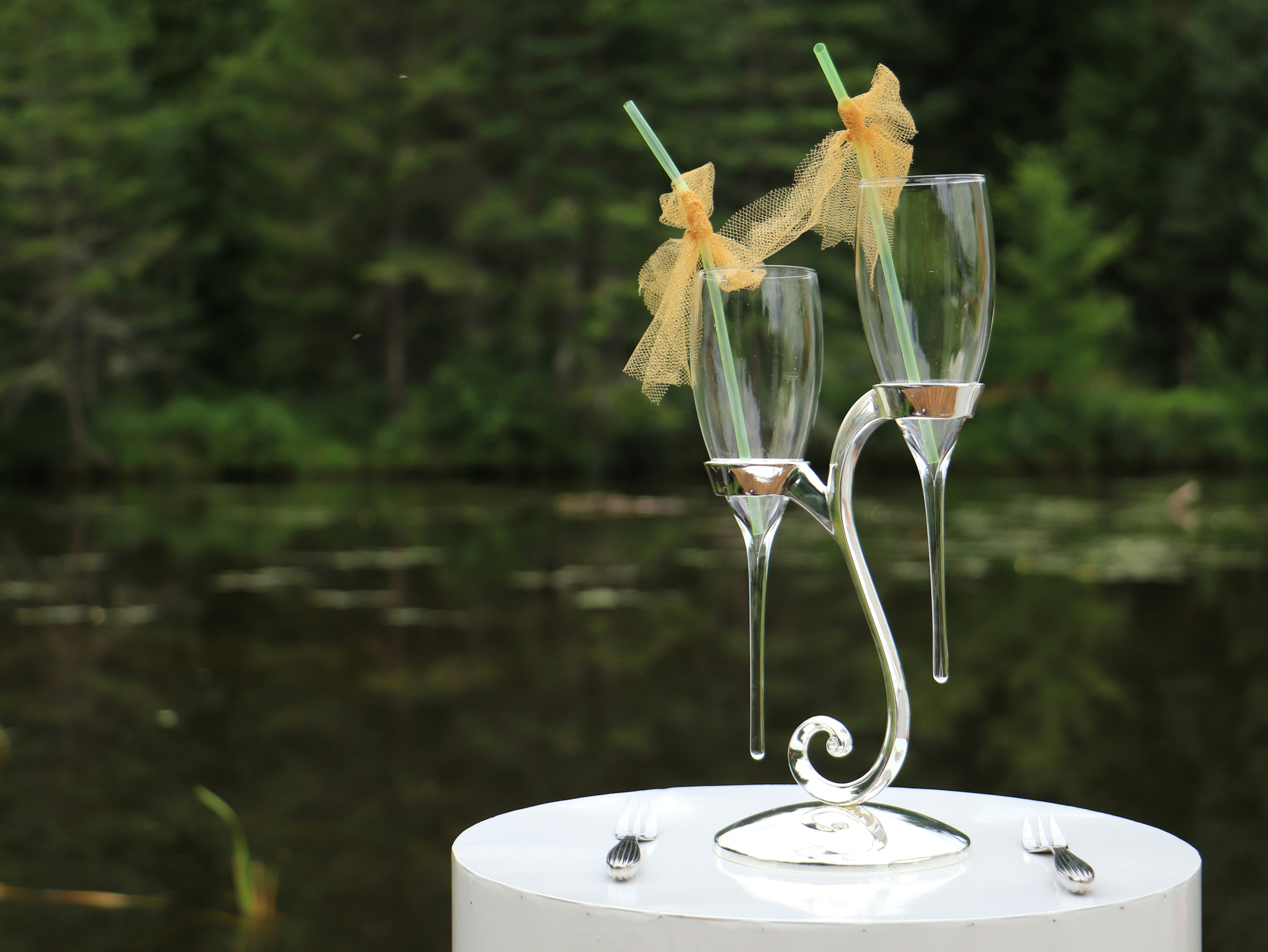 Two elegantly arranged champagne flutes adorned with golden tulle sit atop a white table near a serene water backdrop.