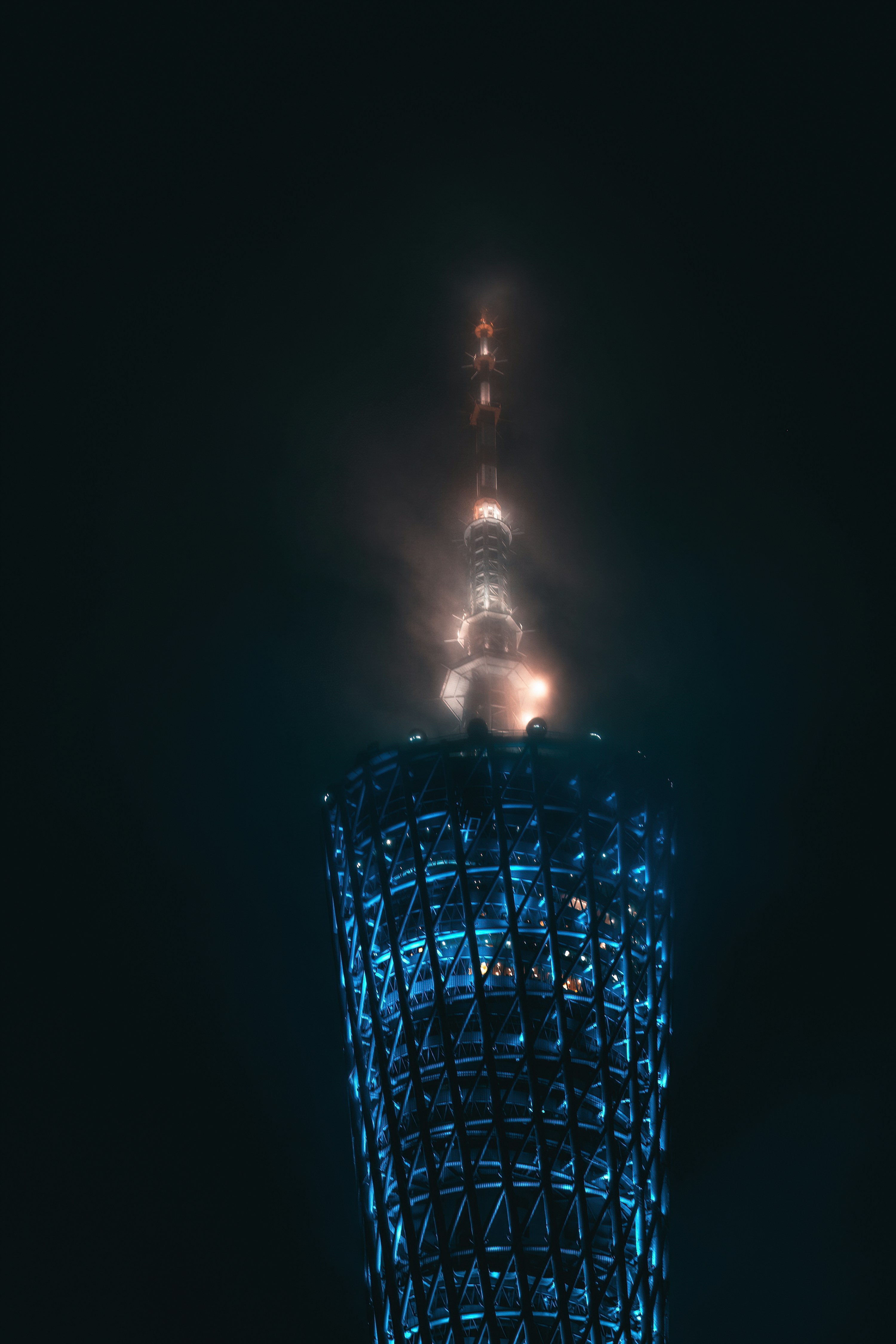 The Tokyo Skytree pierces the night sky, its intricate lattice structure glowing with blue light amidst a veil of fog. A beacon of modern architecture.