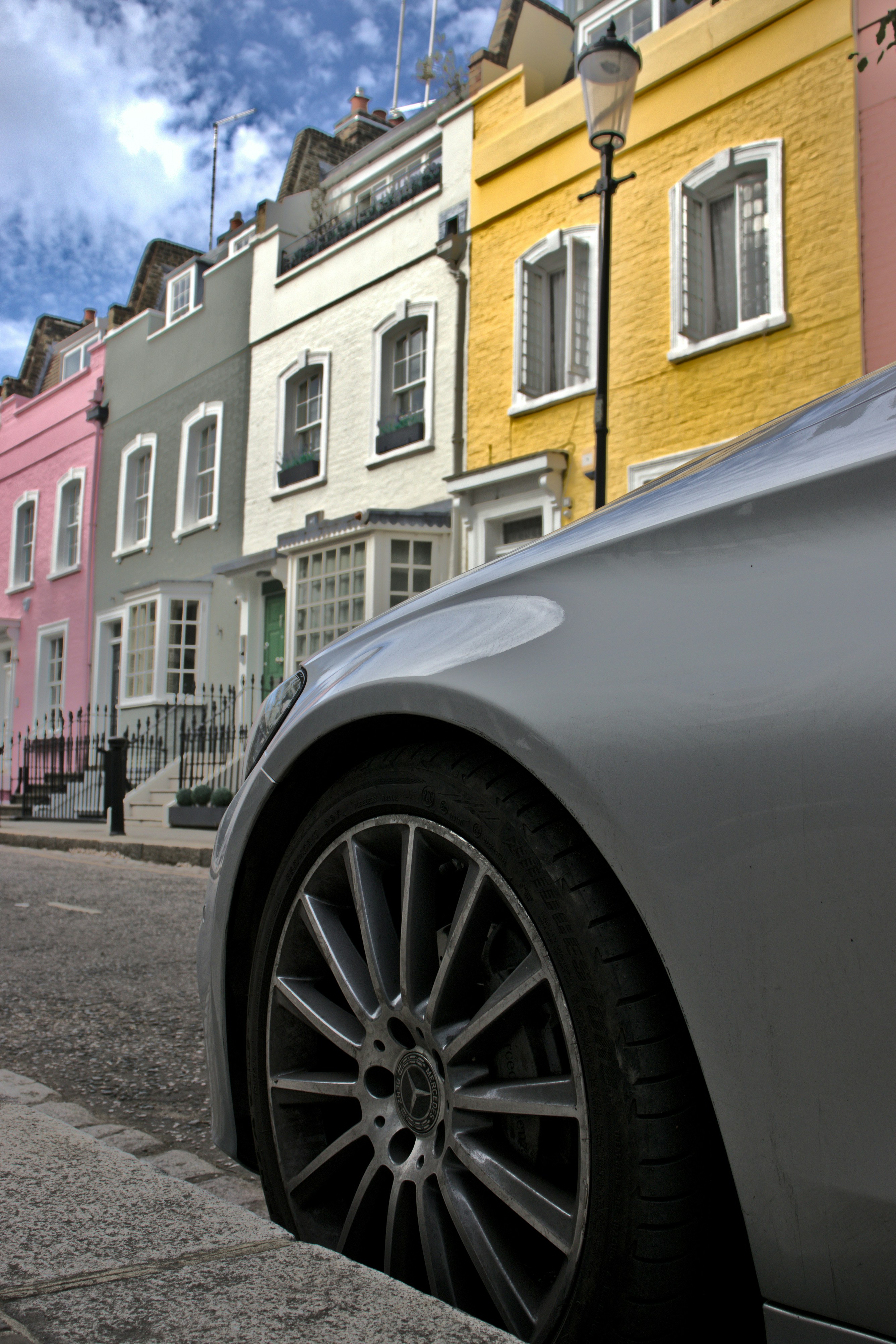Close-up view of a sleek silver car wheel with colorful pastel houses in the background, showcasing urban architecture.