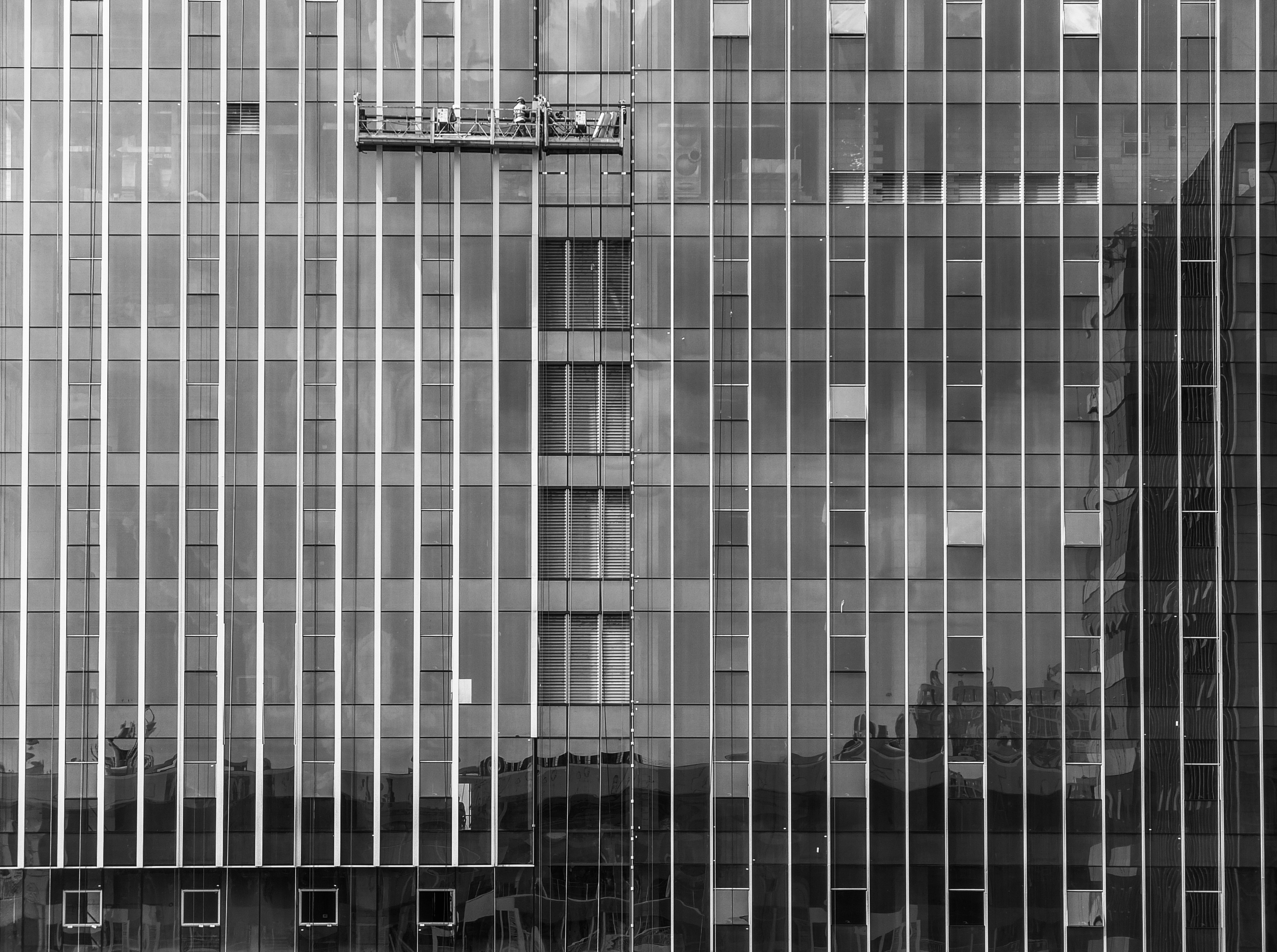 Glass façade of a high-rise building under construction, showcasing scaffolding and reflections of the surrounding environment.